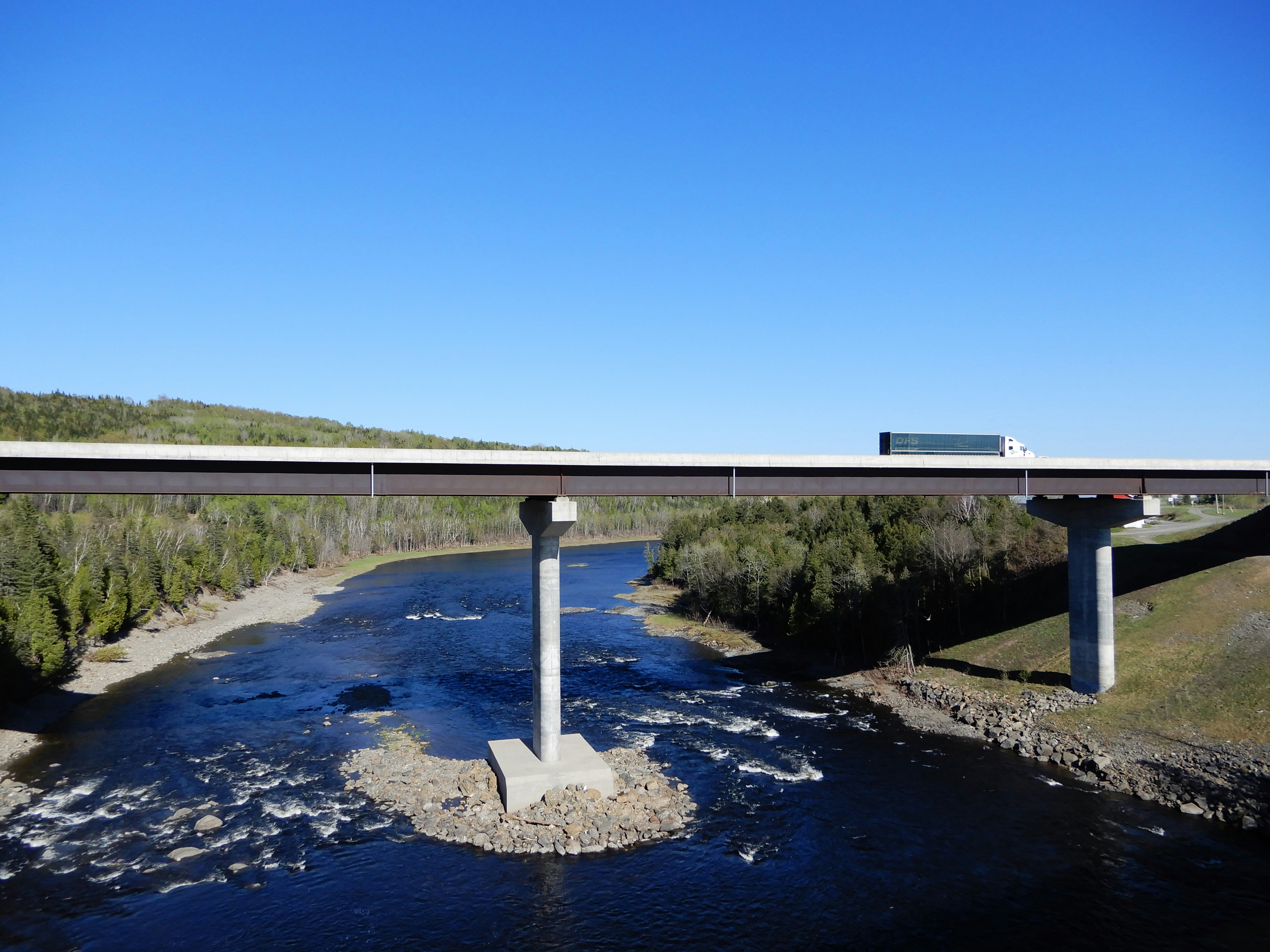 Bridge spanning a tranquil river with lush greenery under a clear blue sky.