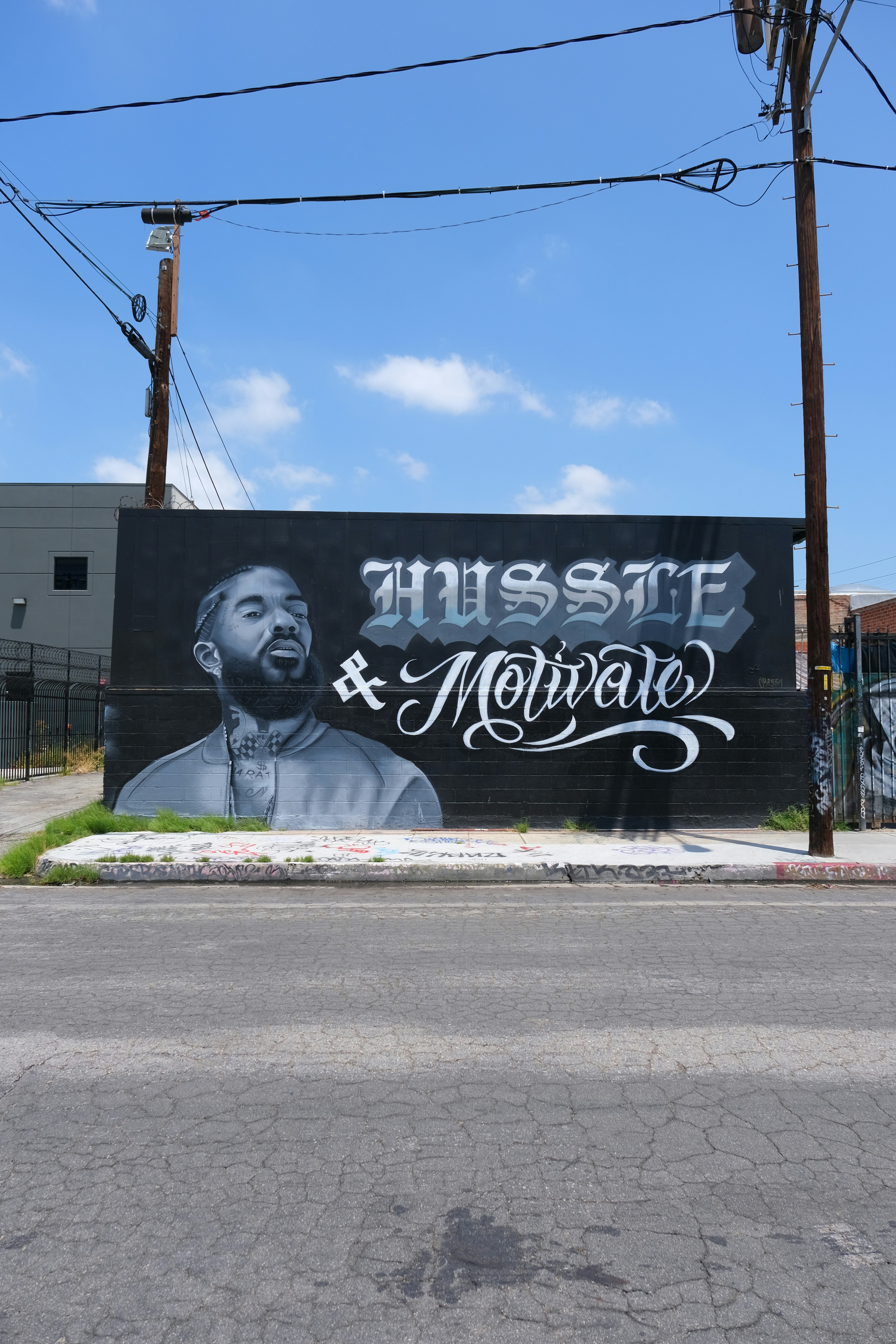 Black and white mural depicting a figure with tattoos and the words 'Hussle & Motivate' prominently displayed. The artwork reflects themes of determination and empowerment.