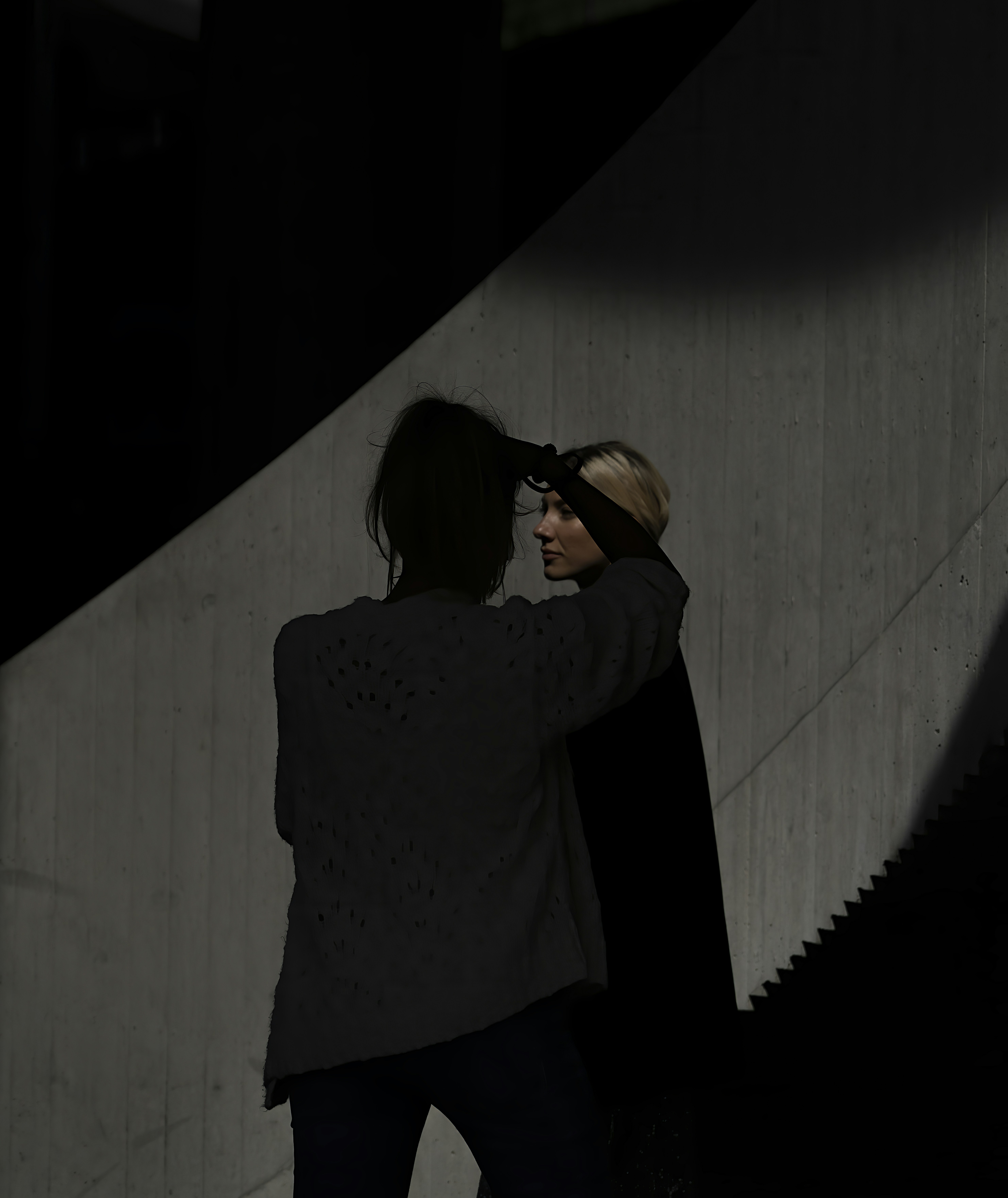 Quiet Exchange in Diagonal Light on a Concrete Stairwell