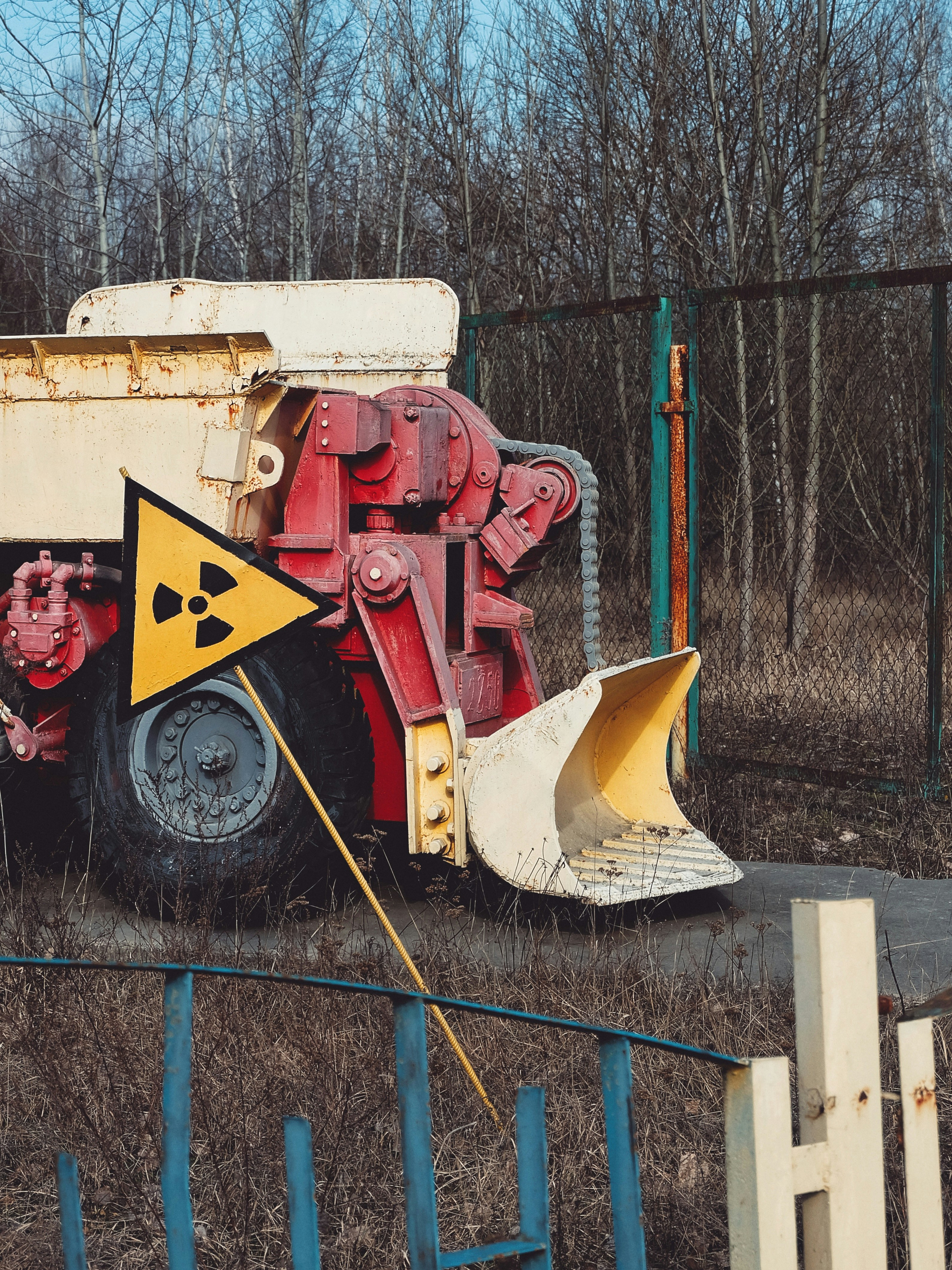 Abandoned machinery with a radiation warning sign, surrounded by barren grass and a rusty fence. The scene evokes a sense of desolation and forgotten history.