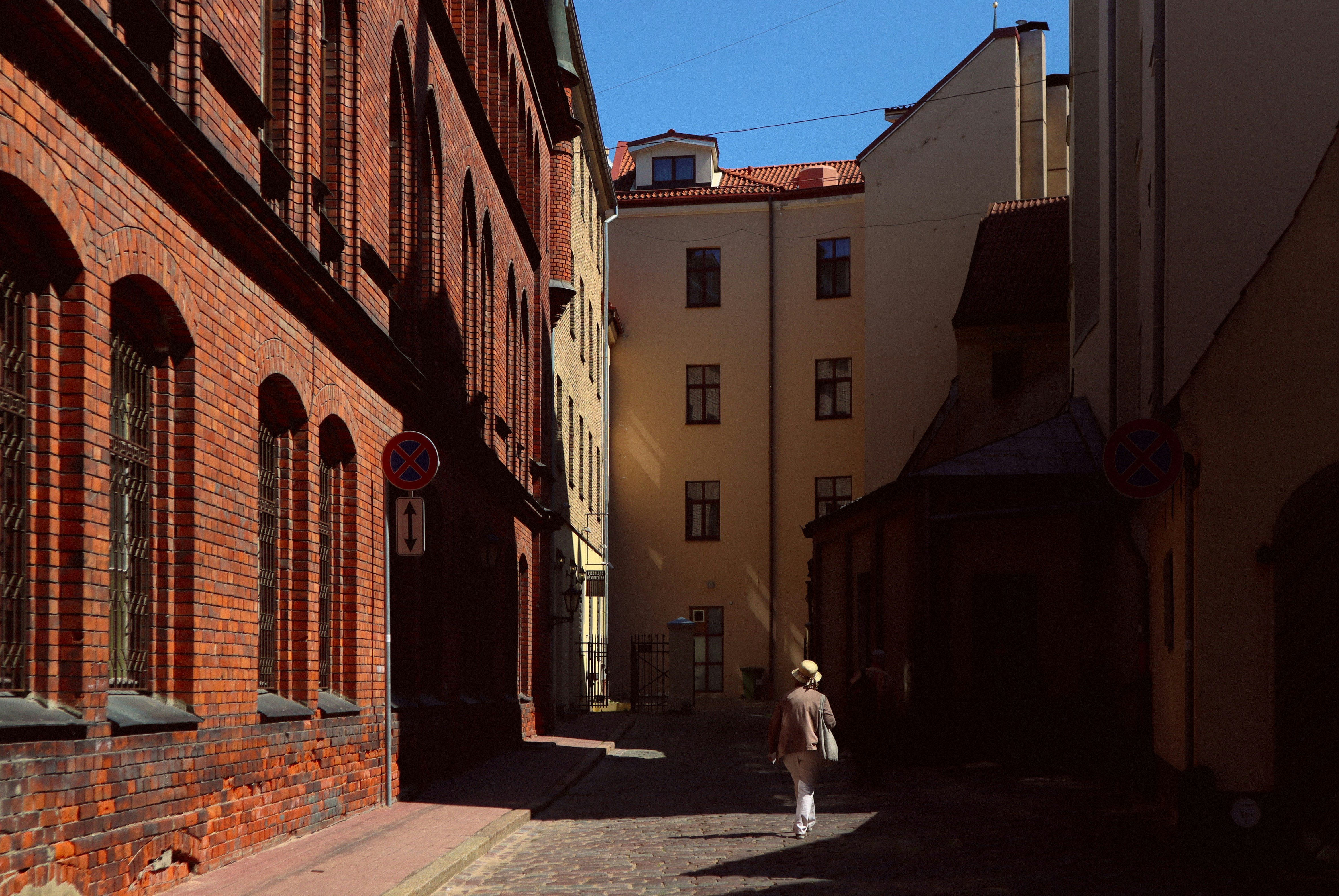 Sunlit Cobblestone Alley: A Lone Pedestrian Threads Between Brick and Cream Facades