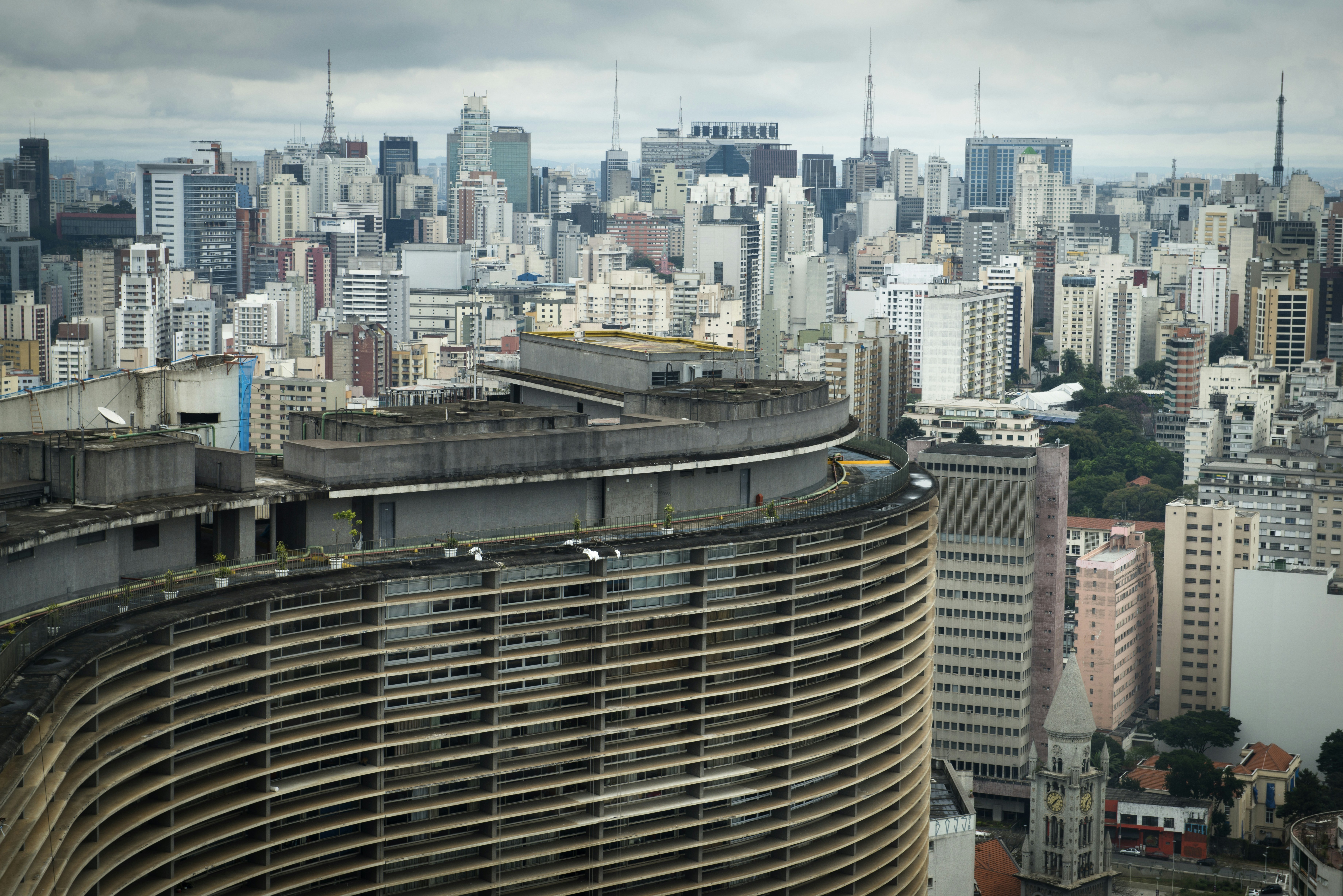 Curved high-rise buildings dominate a sprawling cityscape under a cloudy sky.