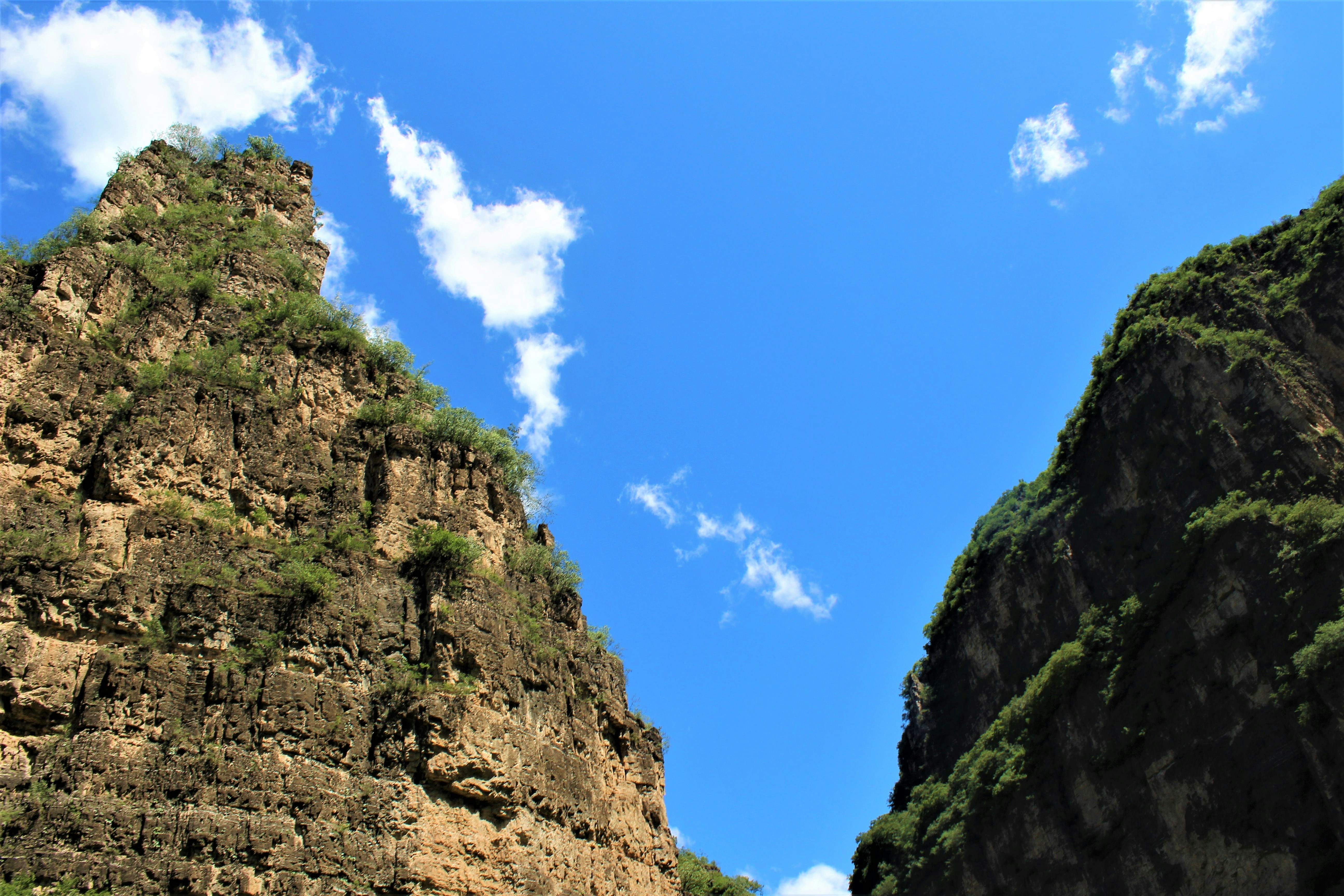 Majestic rocky formations rise against a vibrant blue sky, adorned with patches of greenery. The scene captures the raw beauty of nature's architecture.