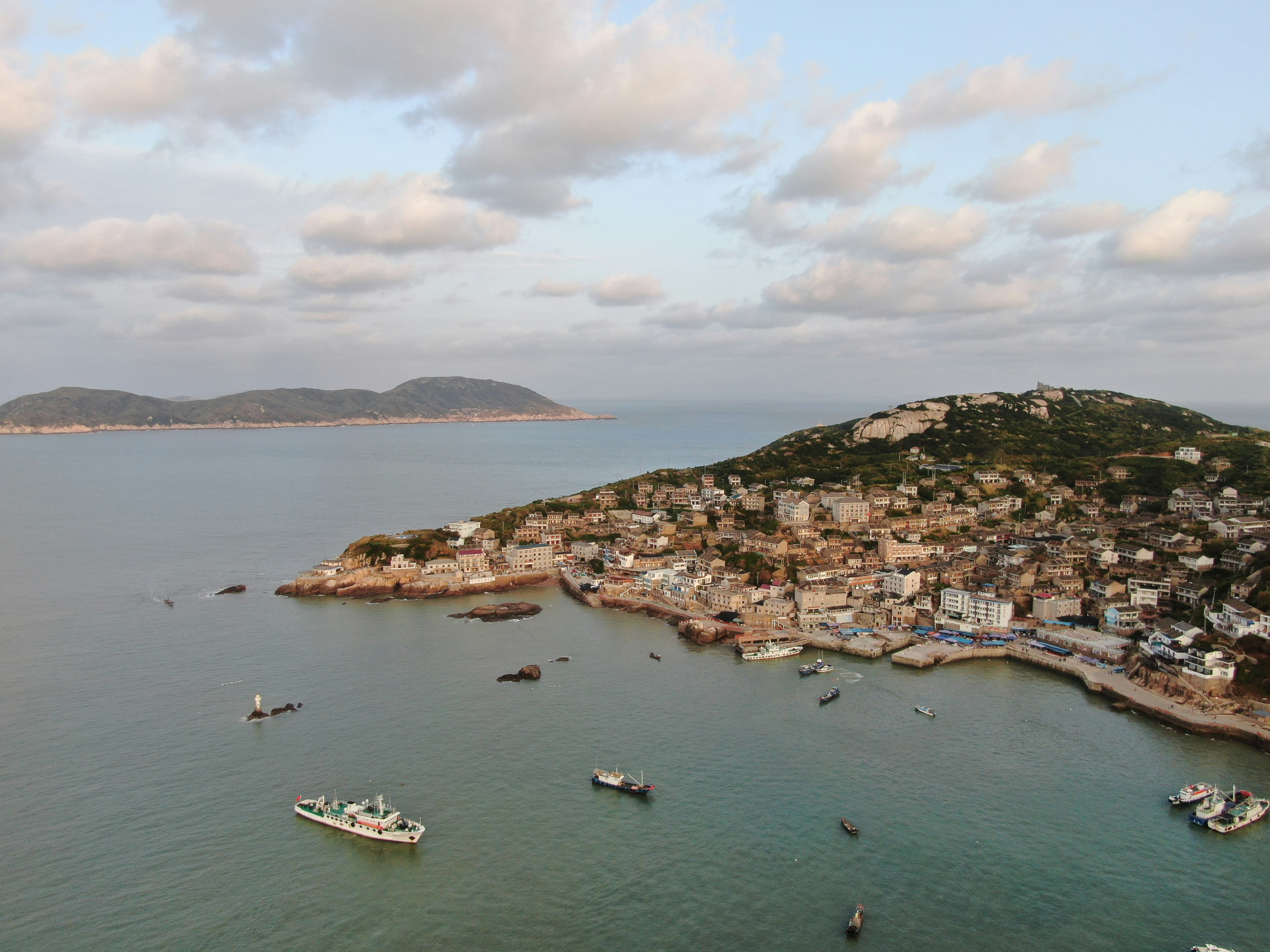Aerial view of a coastal village nestled between land and sea, showcasing boats dotting the water and homes cascading down the hillside.