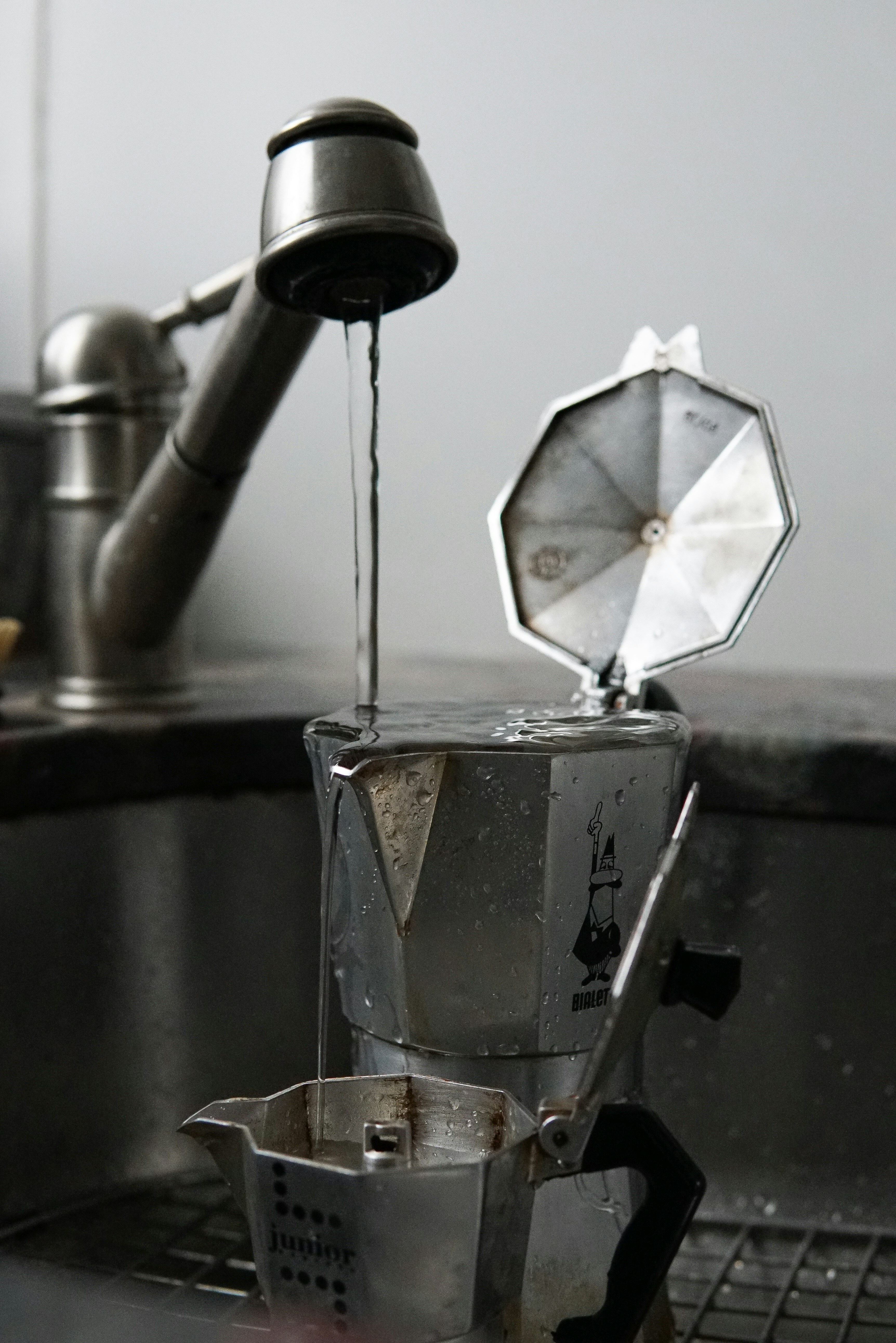Water flows from a faucet into a moka pot, highlighting the brewing process in a cozy kitchen setting.