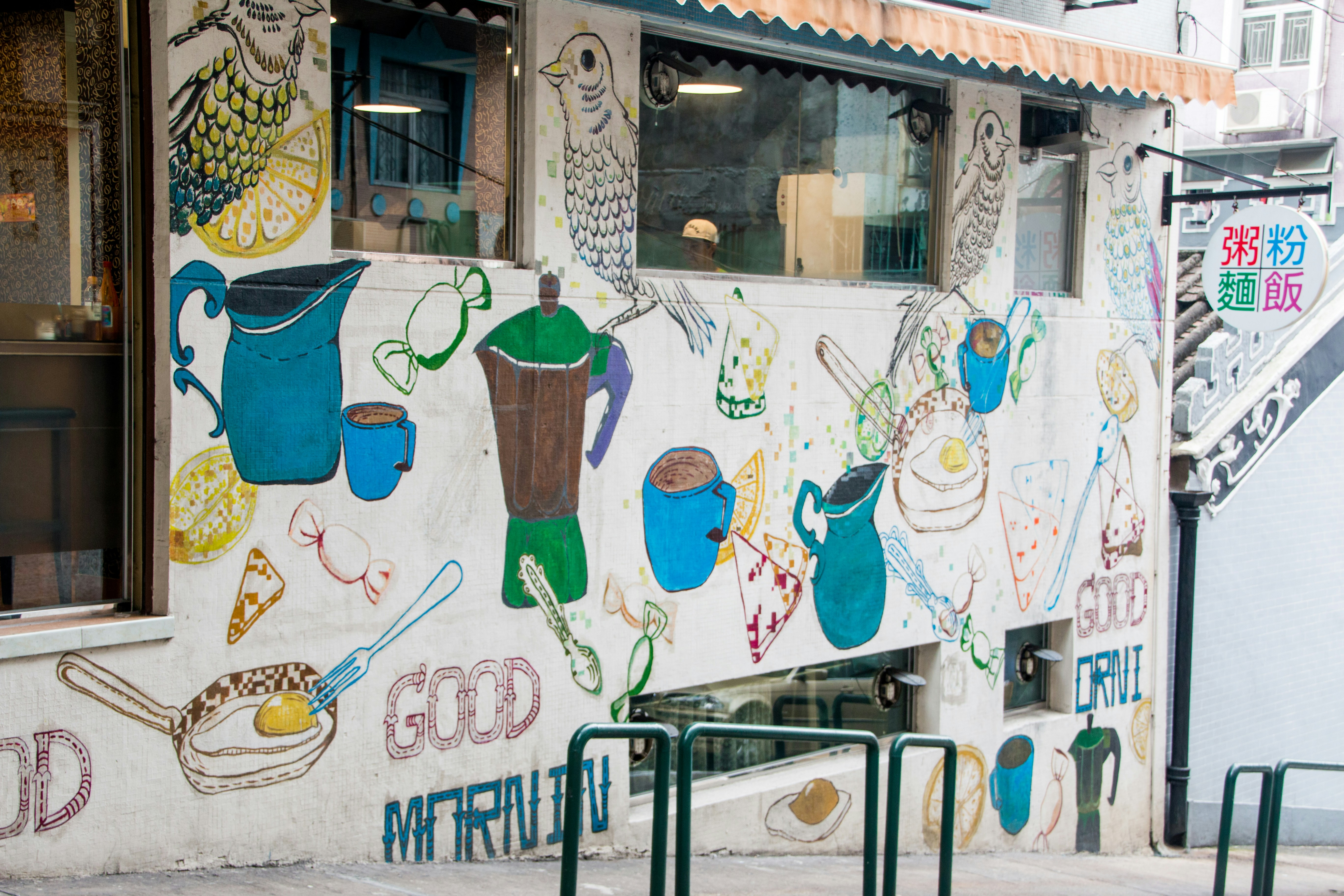 Green-Shirted Anchor in a Whimsical Kitchenware Mural on a Sunlit Stairwell