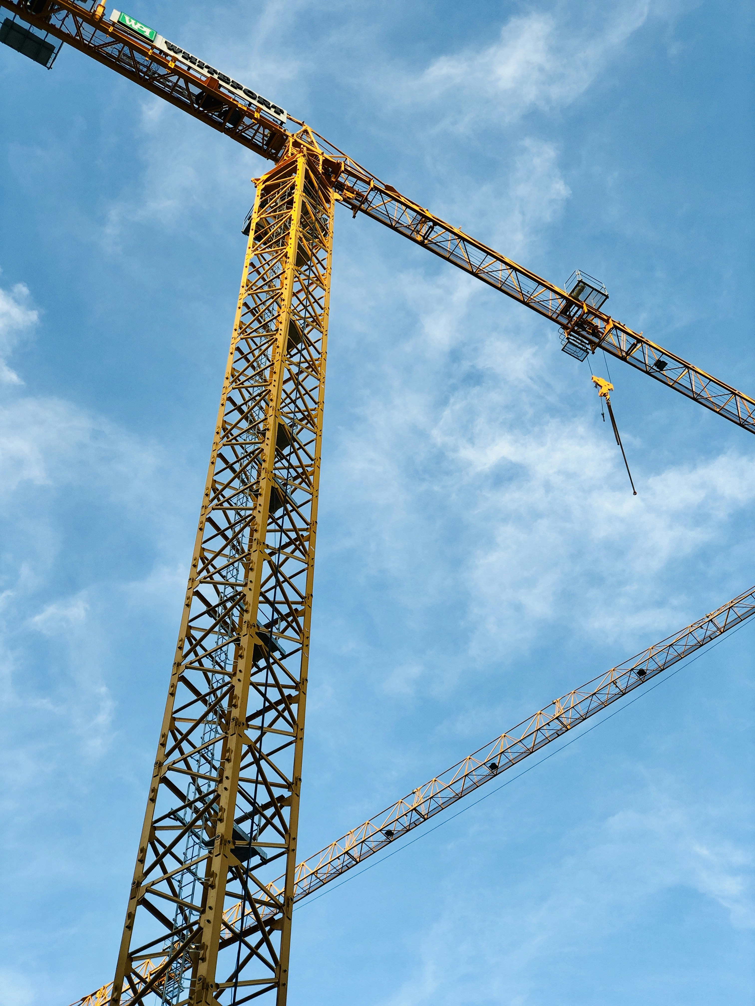 Yellow construction crane towering against a bright blue sky with wispy clouds.