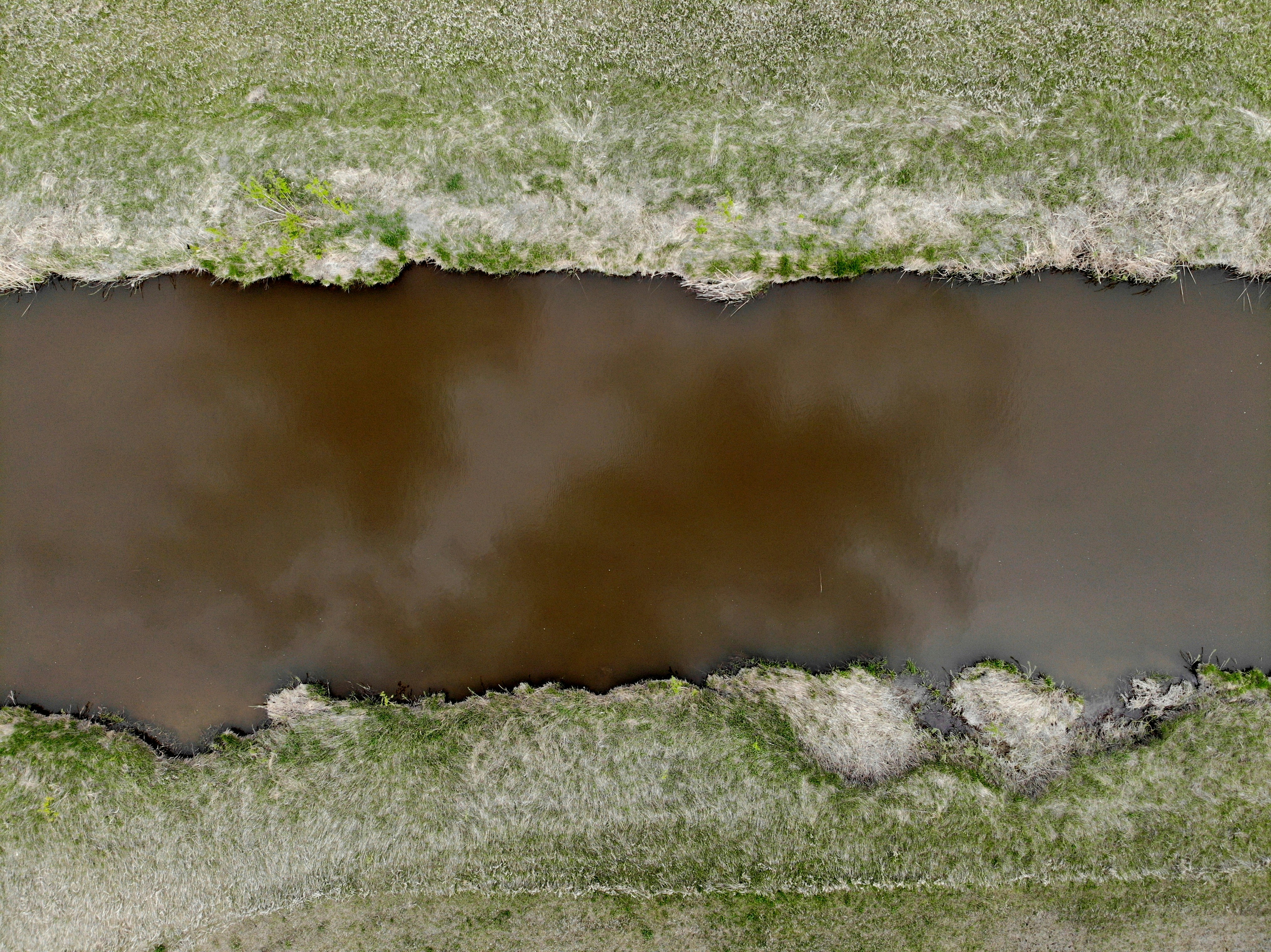 Aerial Snapshot of a Narrow Watercourse Framed by Marshy Banks