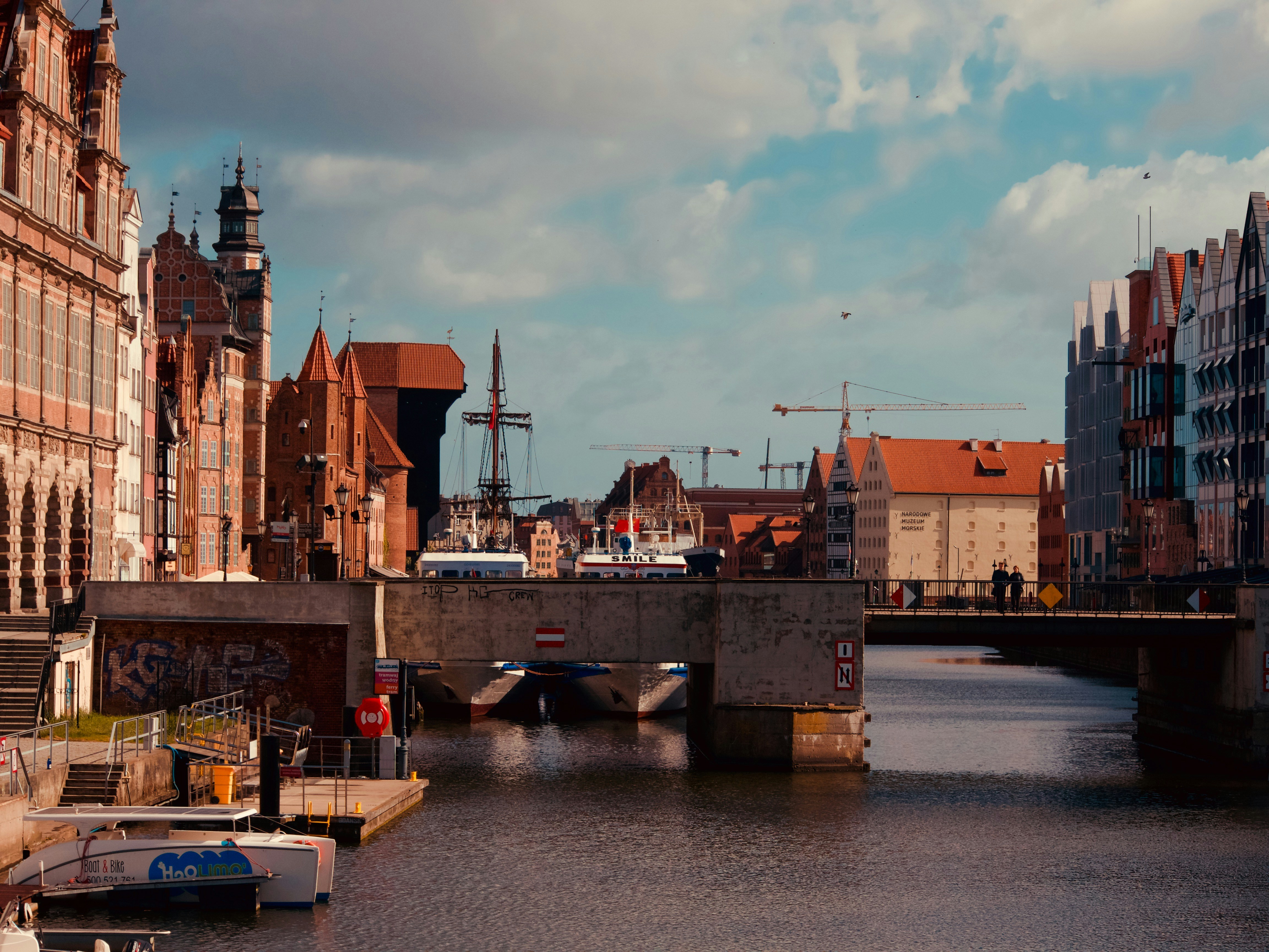Charming waterfront scene in Gdańsk, showcasing a blend of historic and modern buildings along the river. Vibrant boats are moored, reflecting the city's rich maritime heritage.