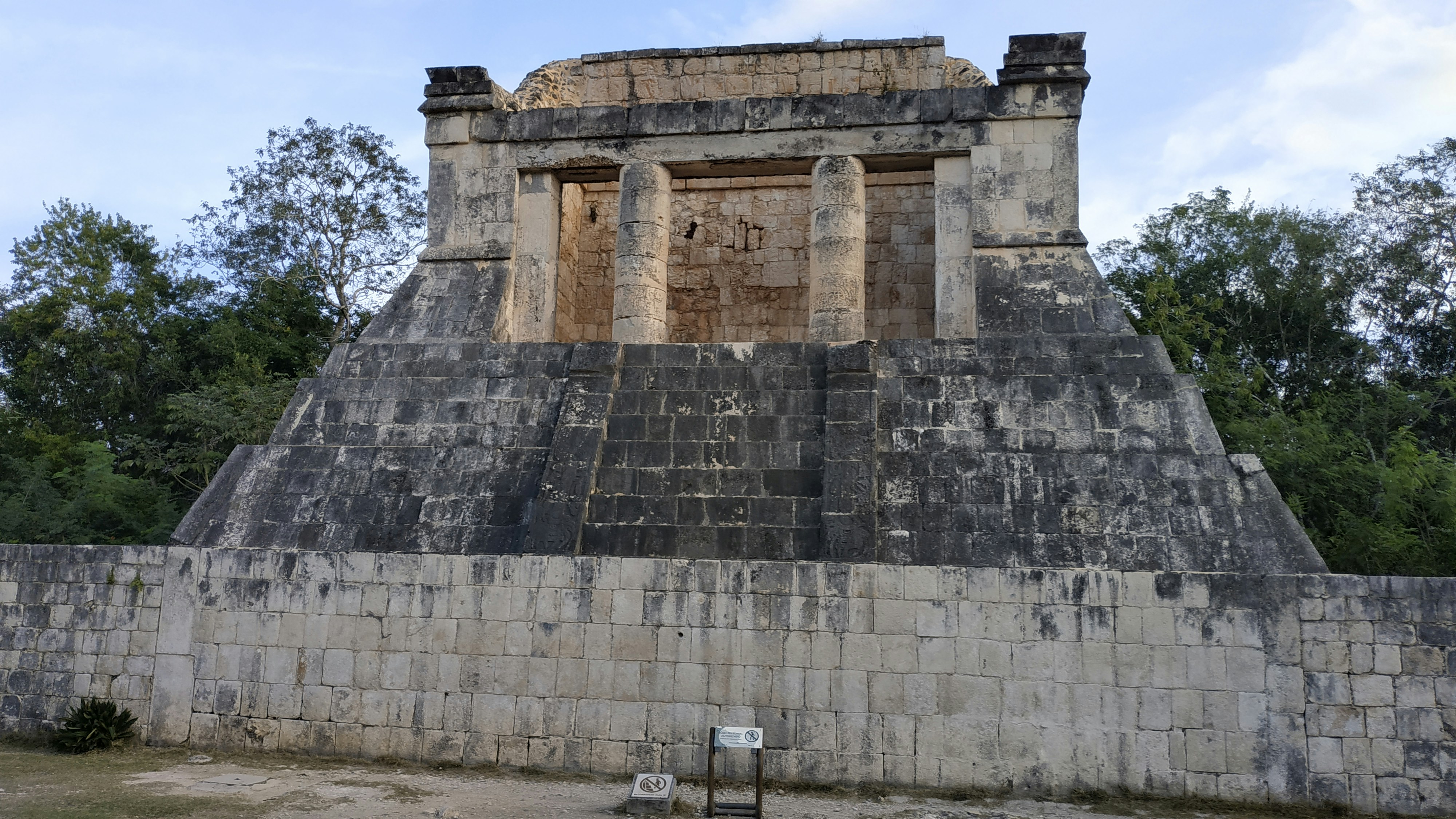 Stone structure with stepped design surrounded by trees under a clear sky.