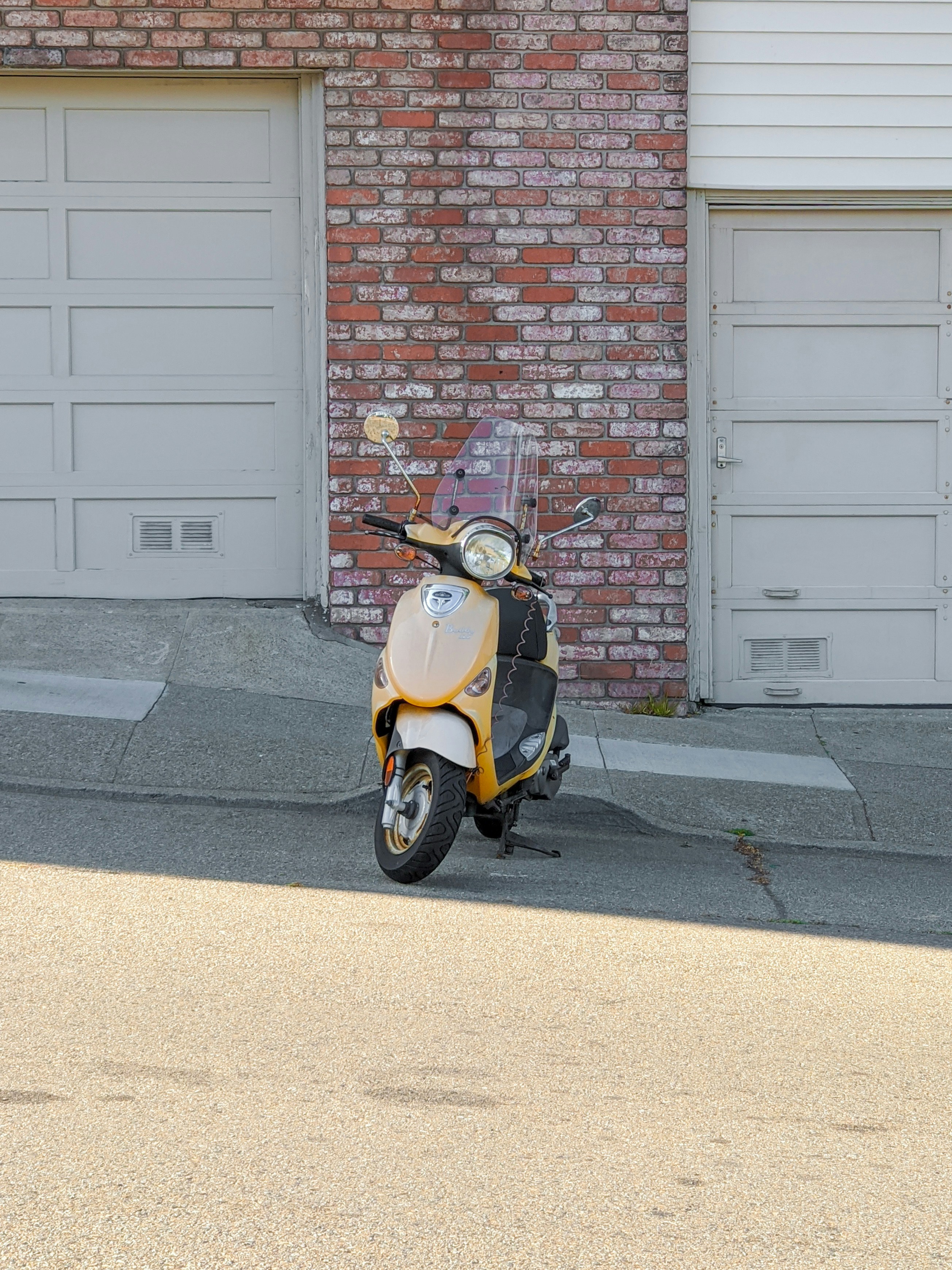 A vibrant yellow scooter parked against a textured brick wall, showcasing urban life and design. The scene captures a moment of stillness in a bustling environment.