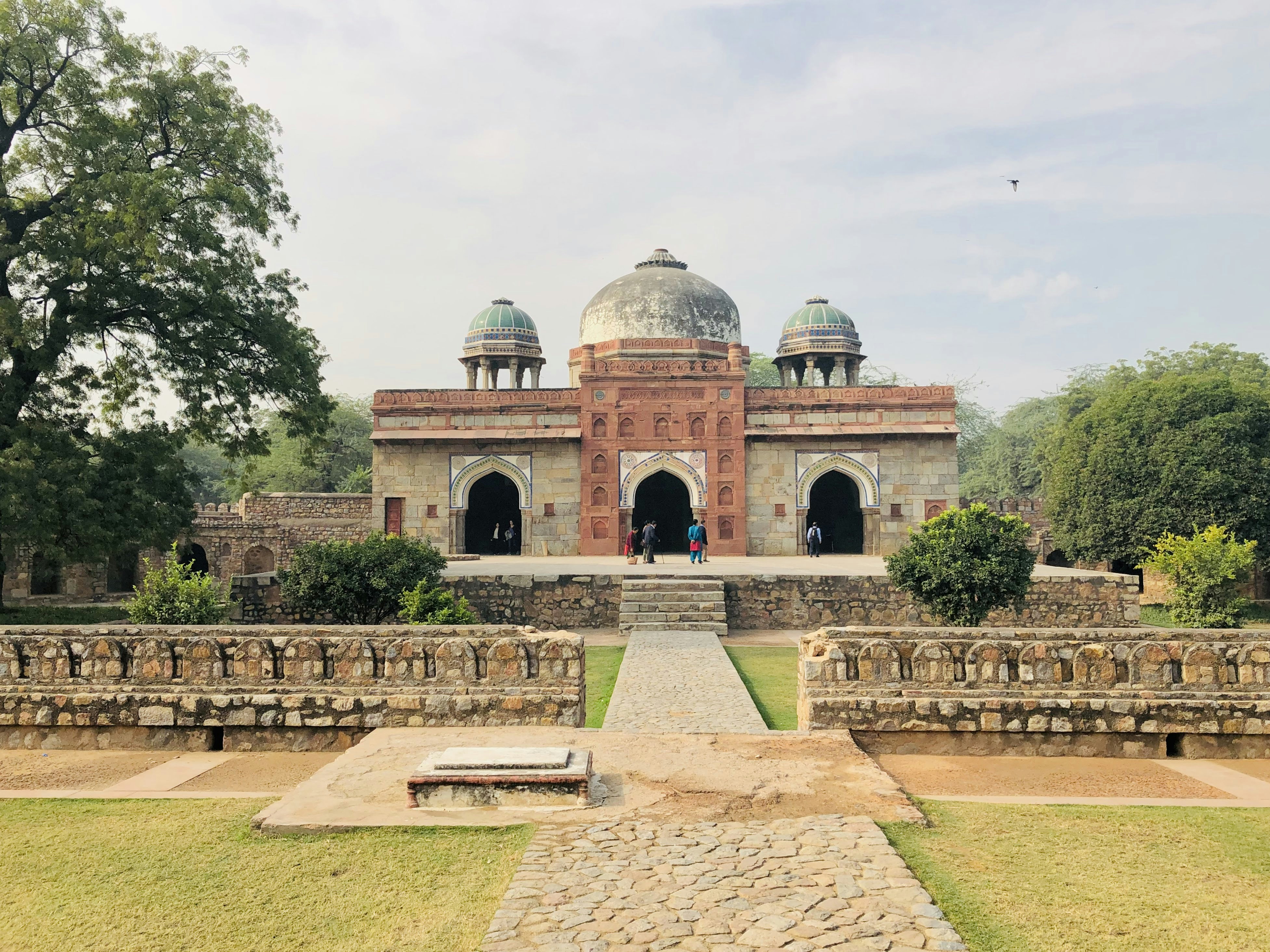 Historic tomb with intricate arches framed by lush greenery and a clear sky.