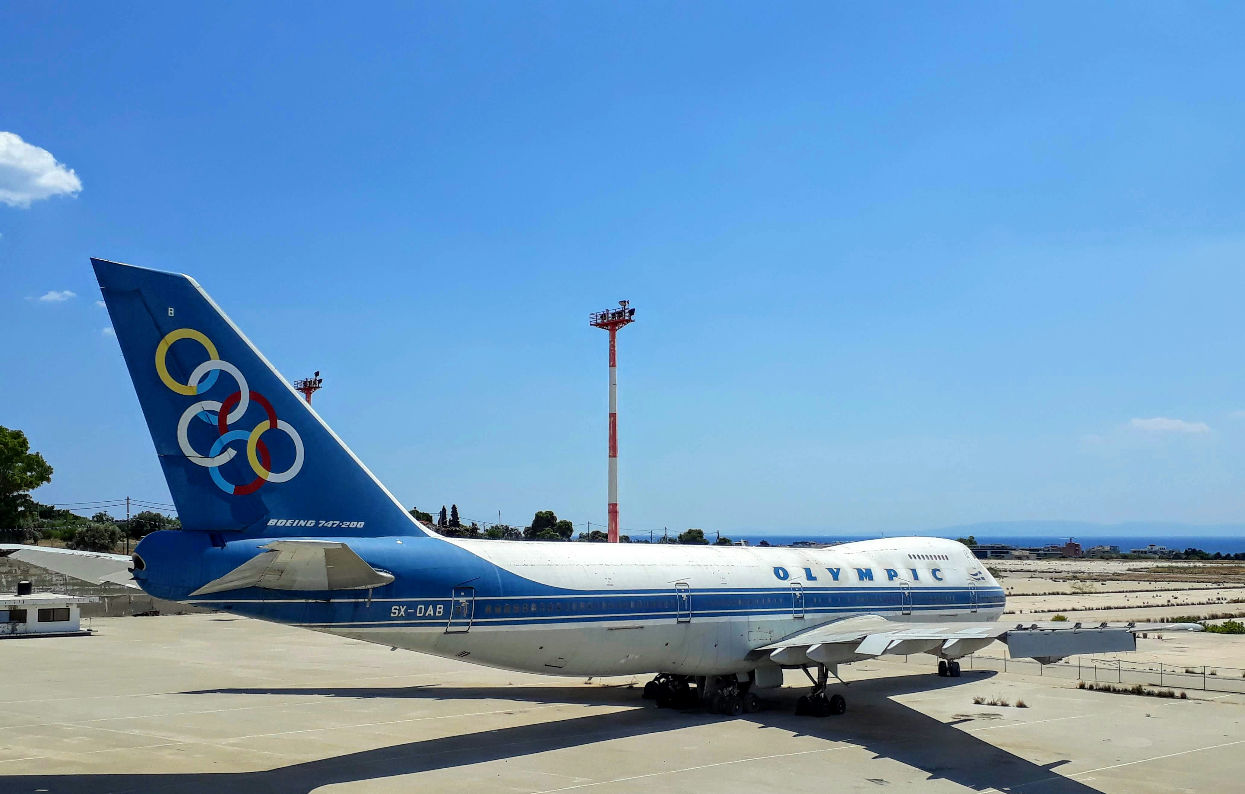 Olympic Airlines Boeing 747 parked at an airport, showcasing its iconic livery against a clear blue sky.