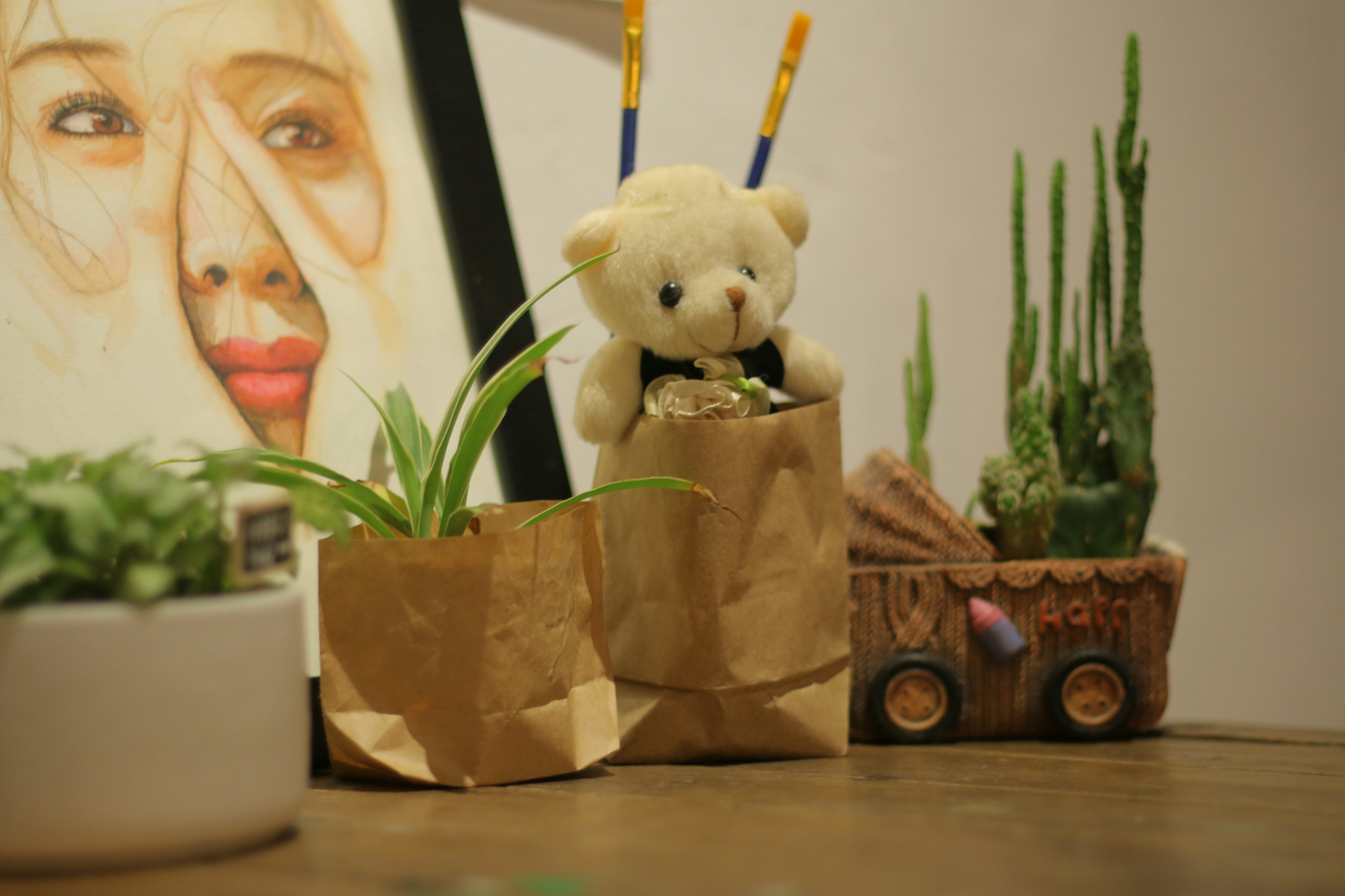 Desk-side Whimsy: Teddy in a Brown Paper Bag Amid Plants and a Painted Portrait