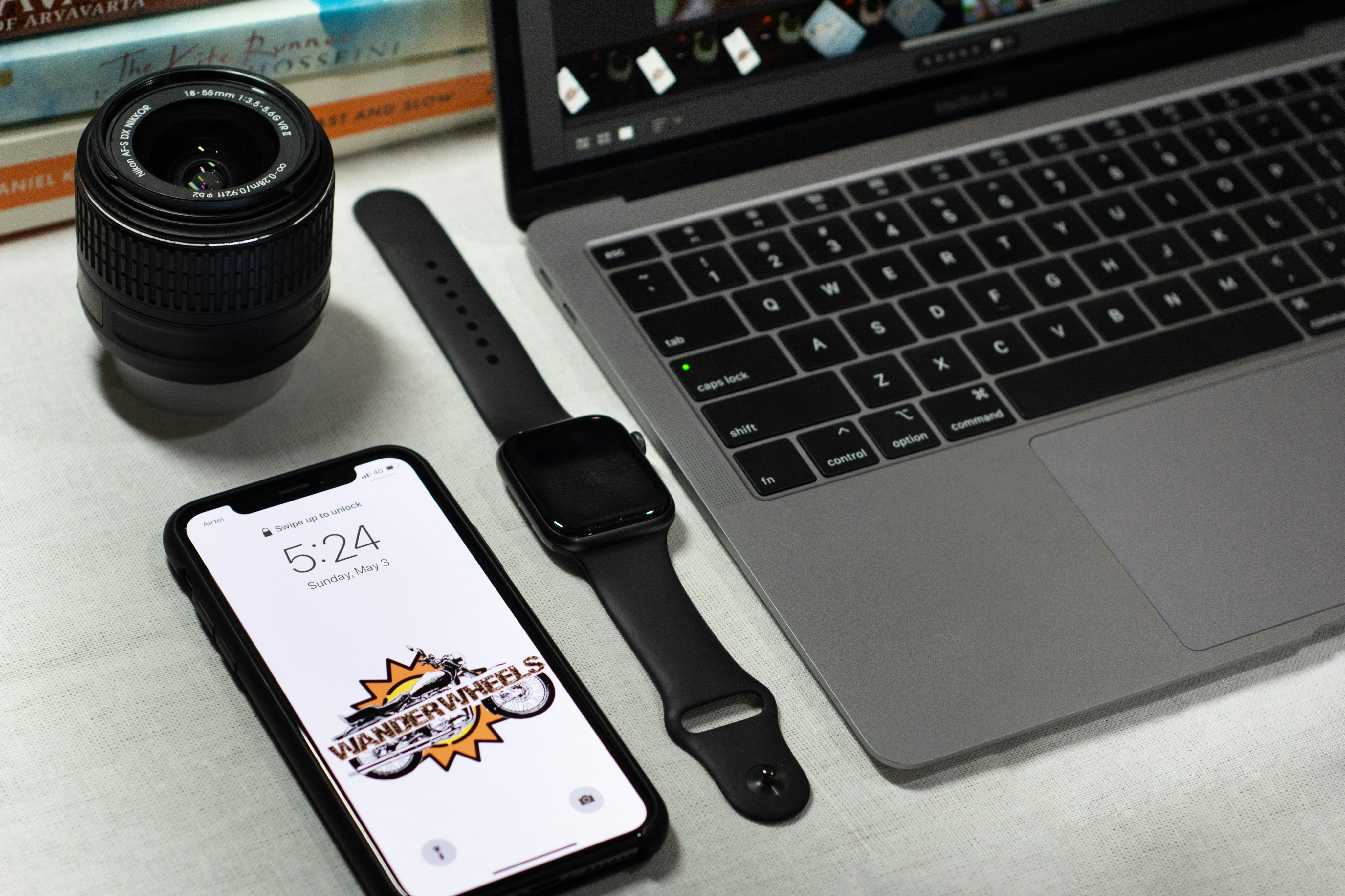 Quiet Tech Atelier: A Lens, a Smartwatch, and a Glowing iPhone on a Laptop Desk