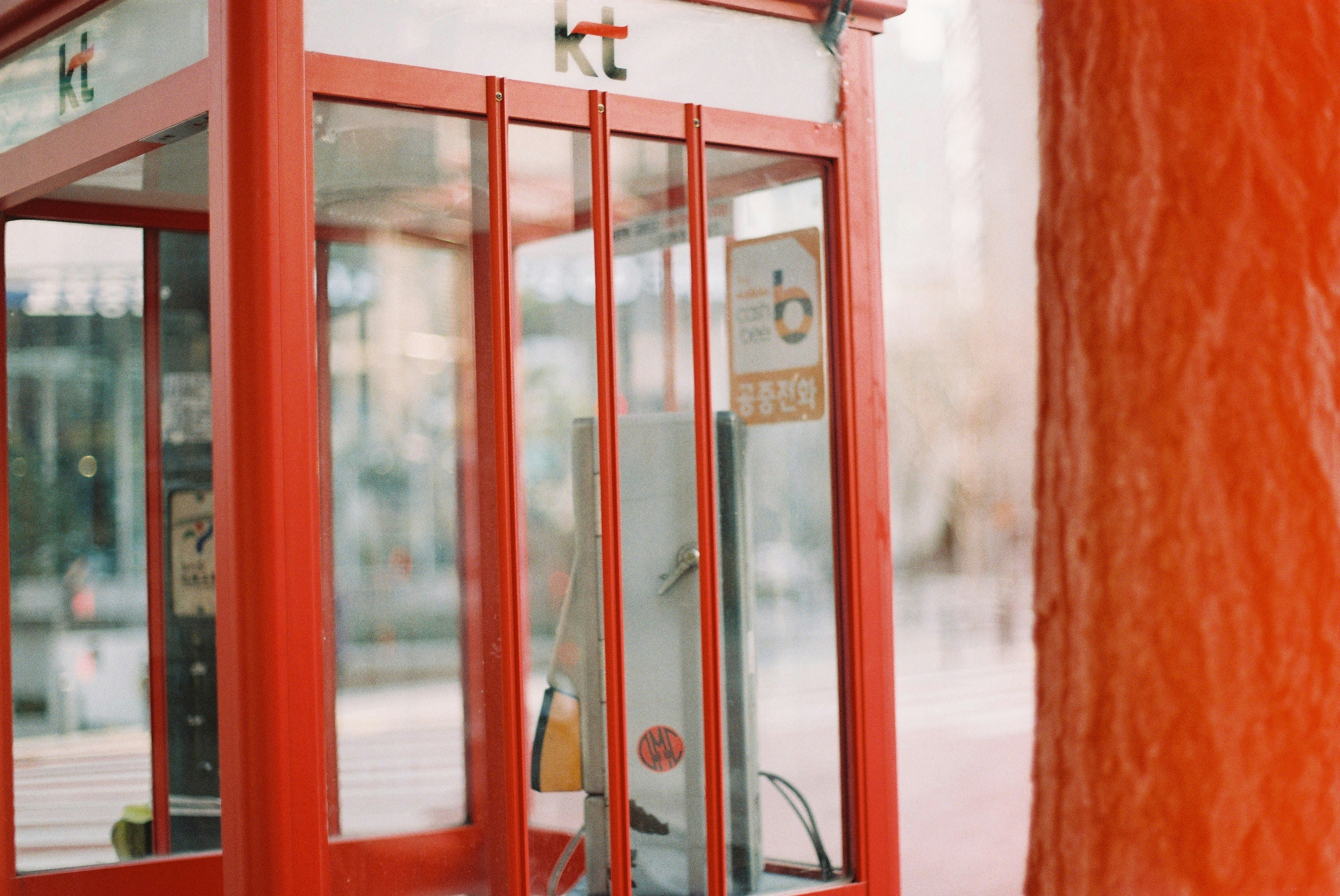 A vintage red phone booth stands prominently, showcasing its glass panels and nostalgic charm. The urban backdrop hints at a bygone era of communication.