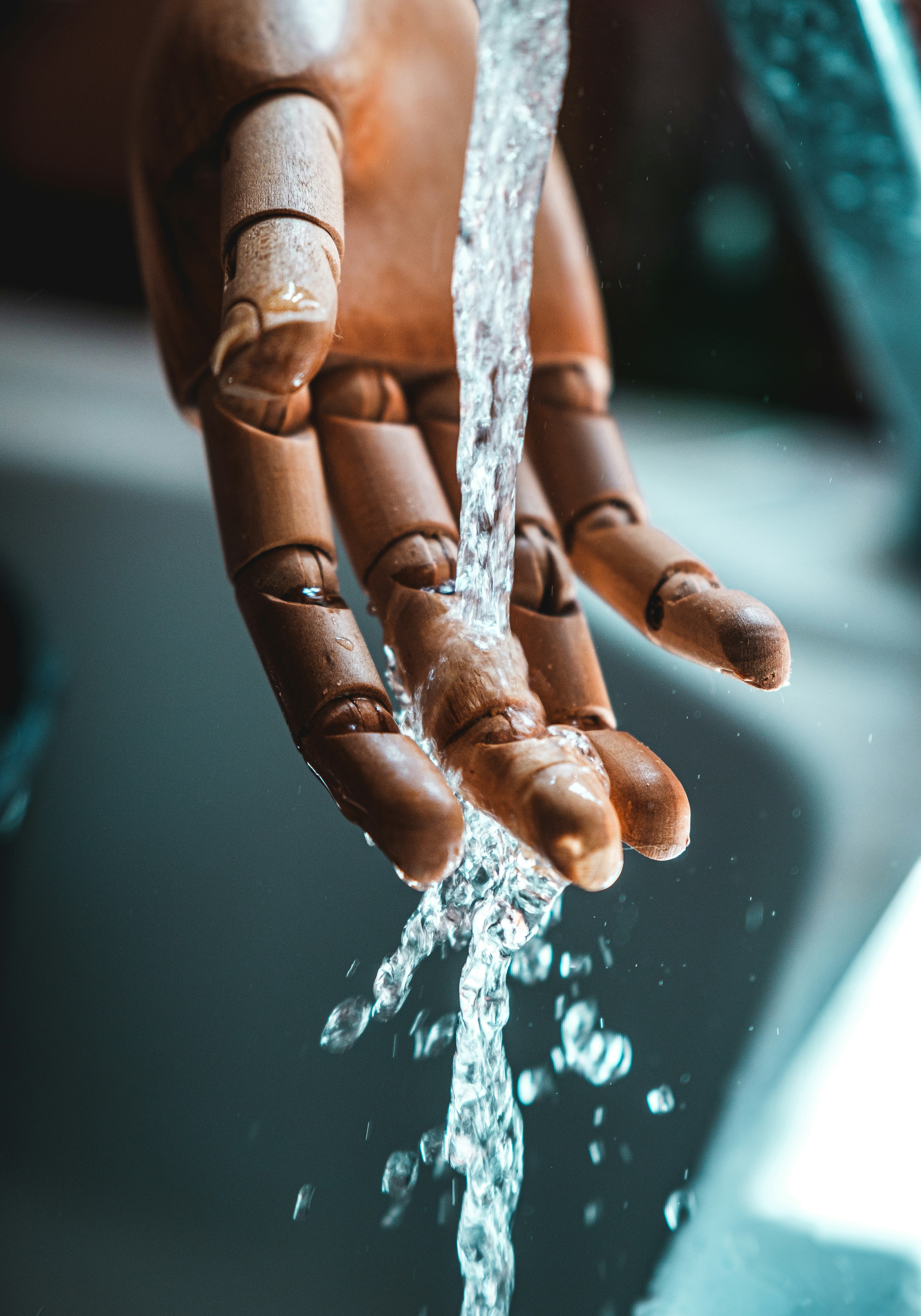 Wooden hand mannequin gracefully catching flowing water in a serene setting.