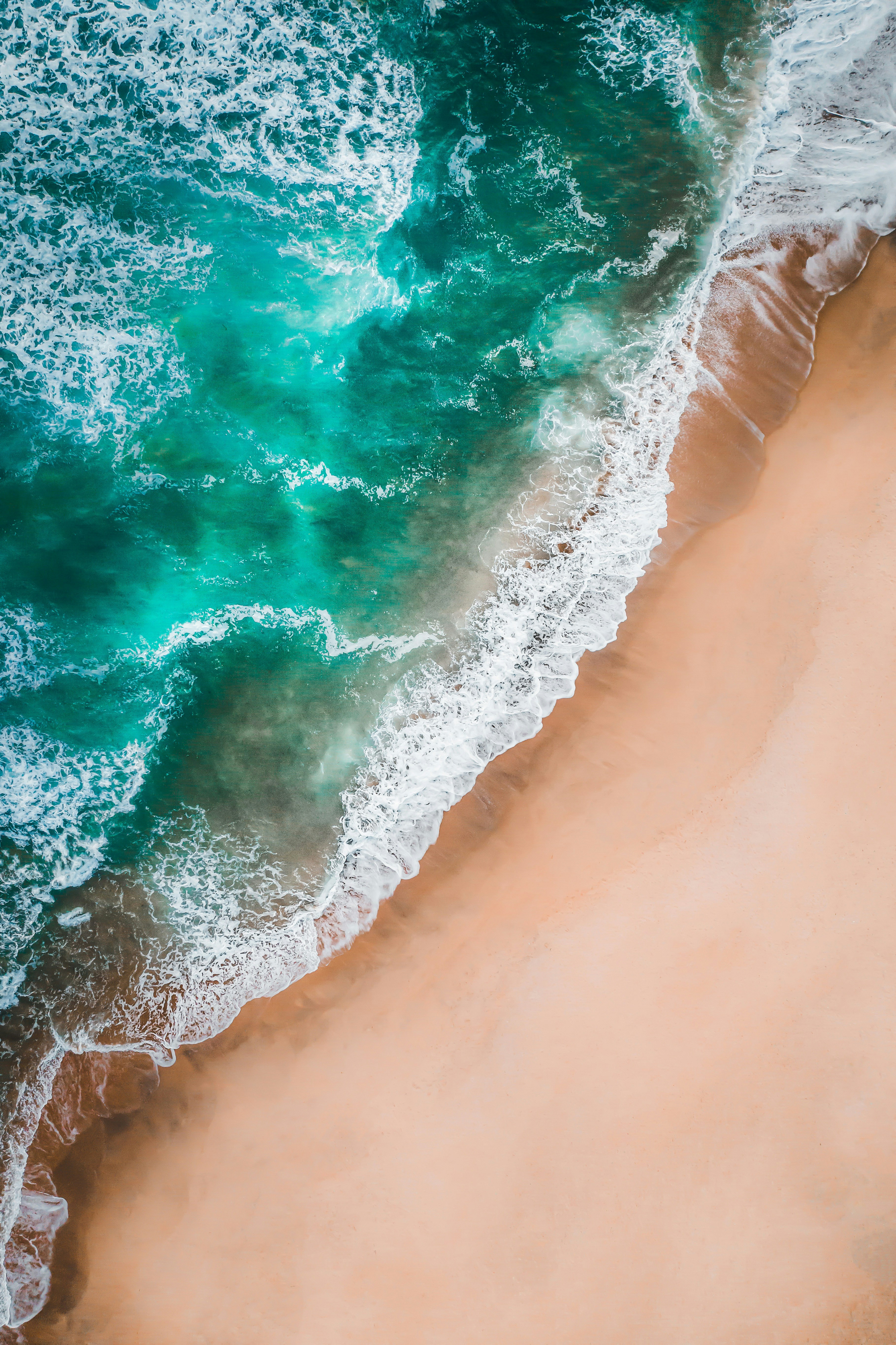 Turquoise waves crashing onto a sandy beach, creating a mesmerizing contrast between water and land. The scene captures the dynamic interplay of nature's elements.