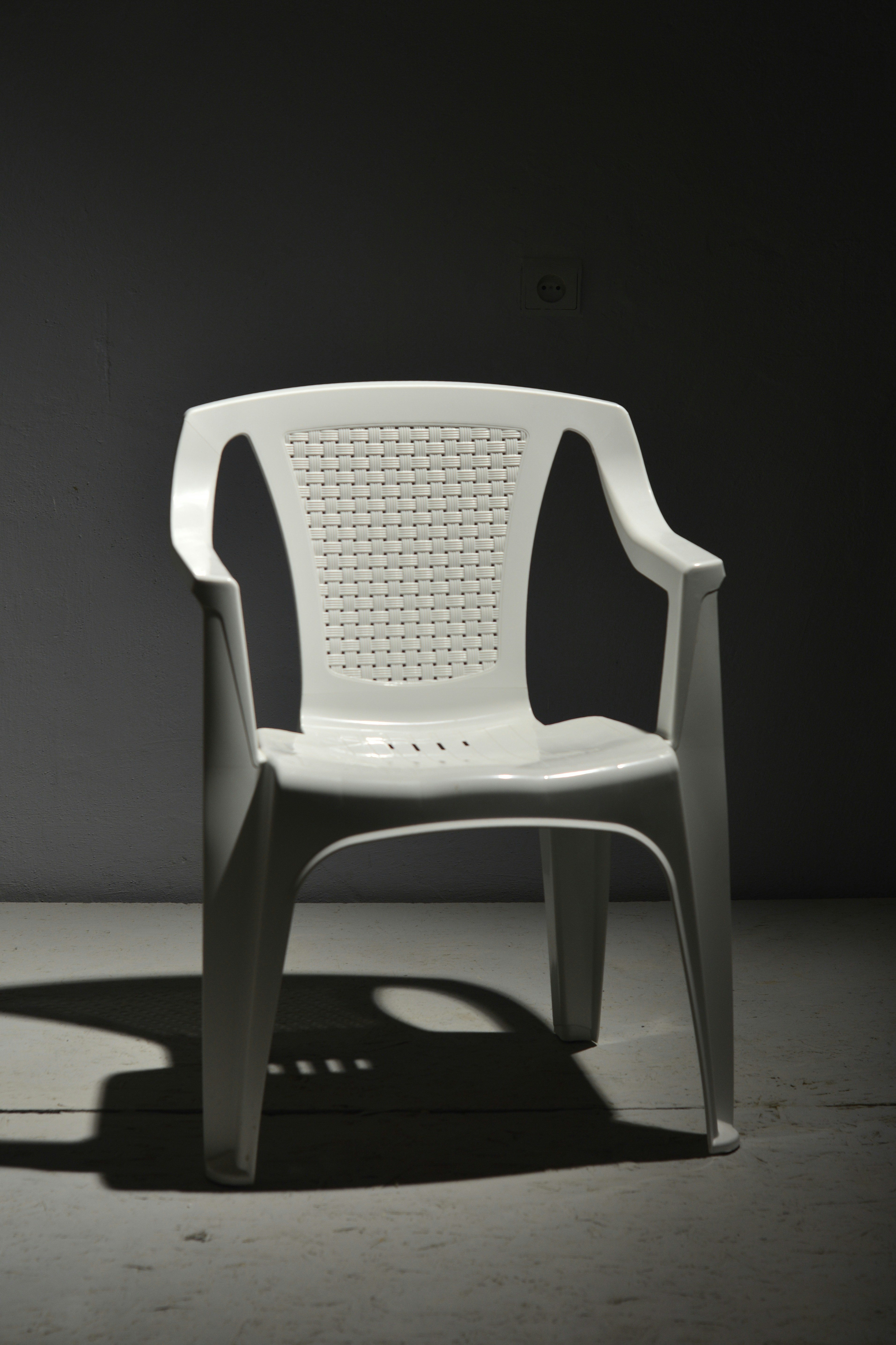White plastic chair casting a distinct shadow on a minimalist background, highlighting its form and texture.