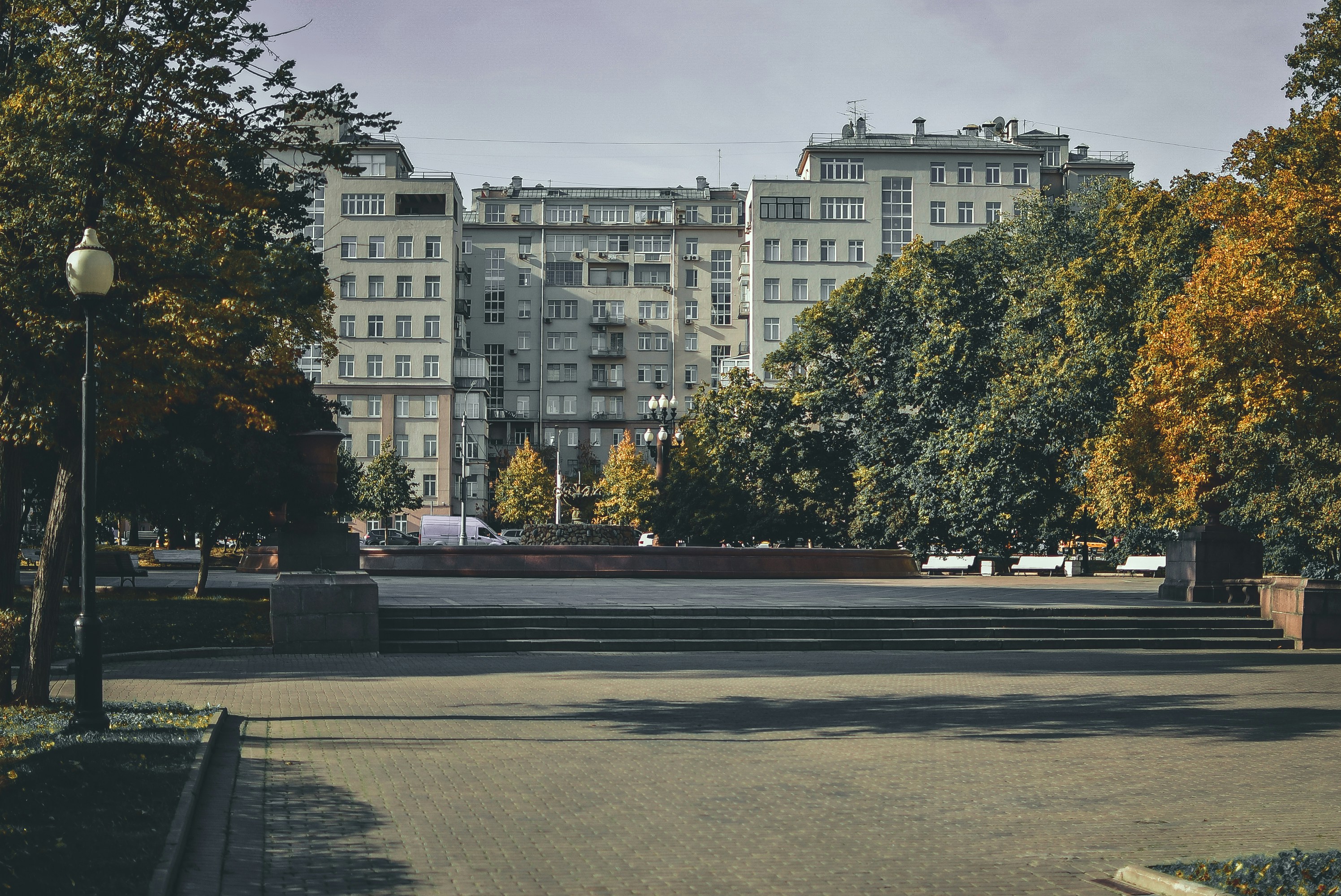 A tranquil urban park scene showcasing vibrant autumn foliage contrasted against a backdrop of modern architecture. The setting invites quiet reflection.