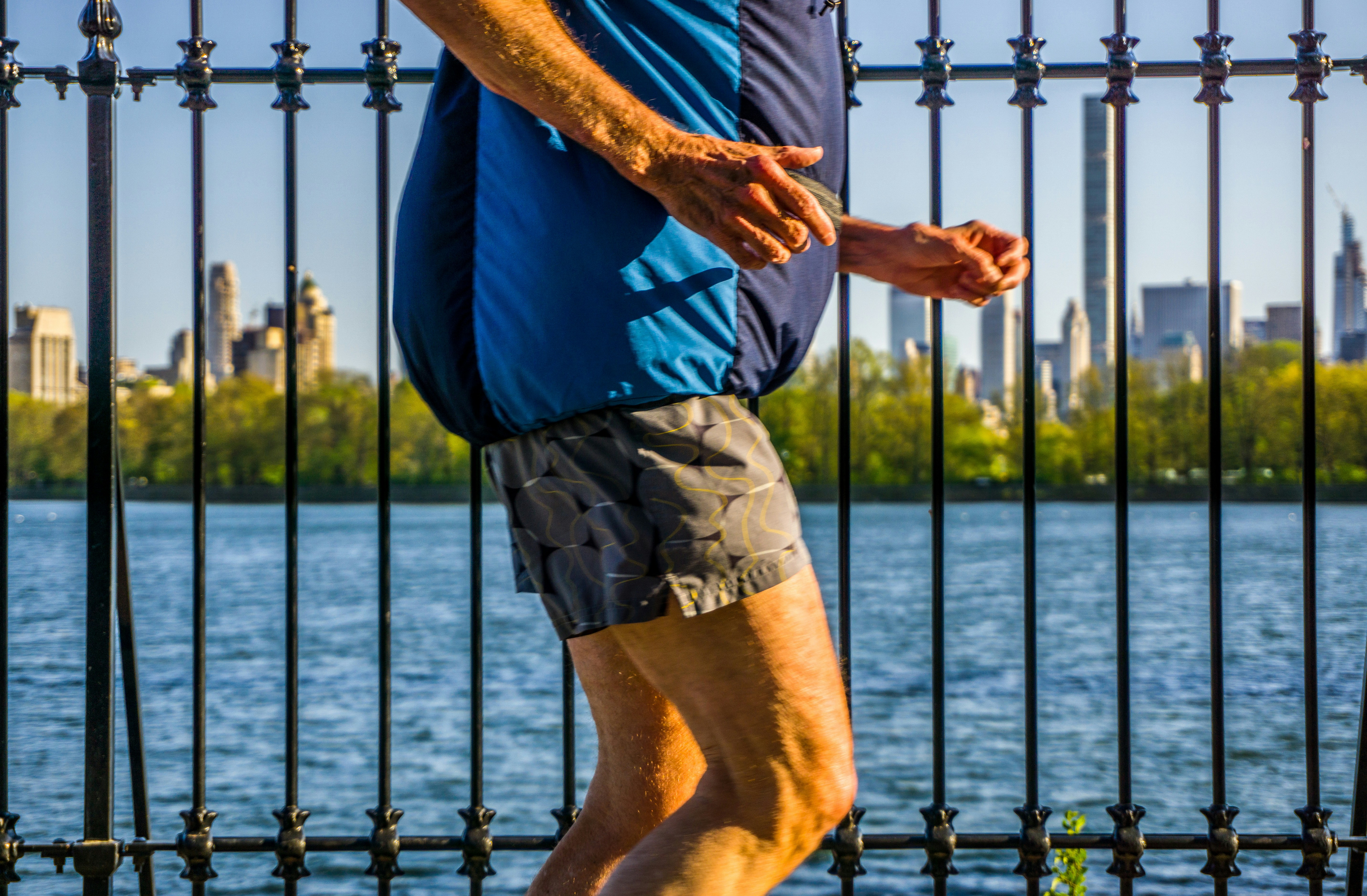 Runner in motion along a waterfront path, framed by a decorative fence with a city skyline in the background.