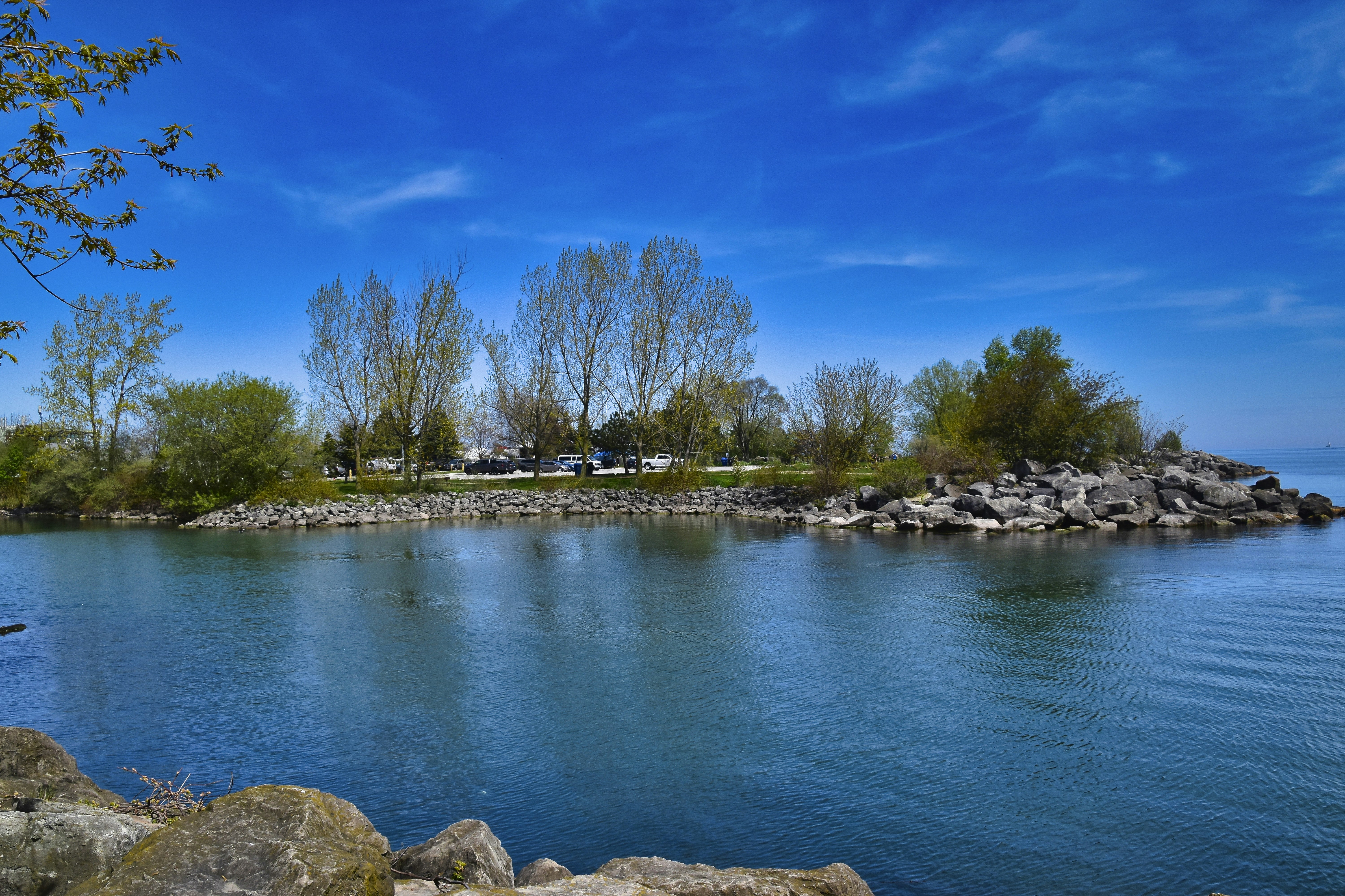 Serene lake bordered by rocky shores and sparse trees under a vibrant blue sky.