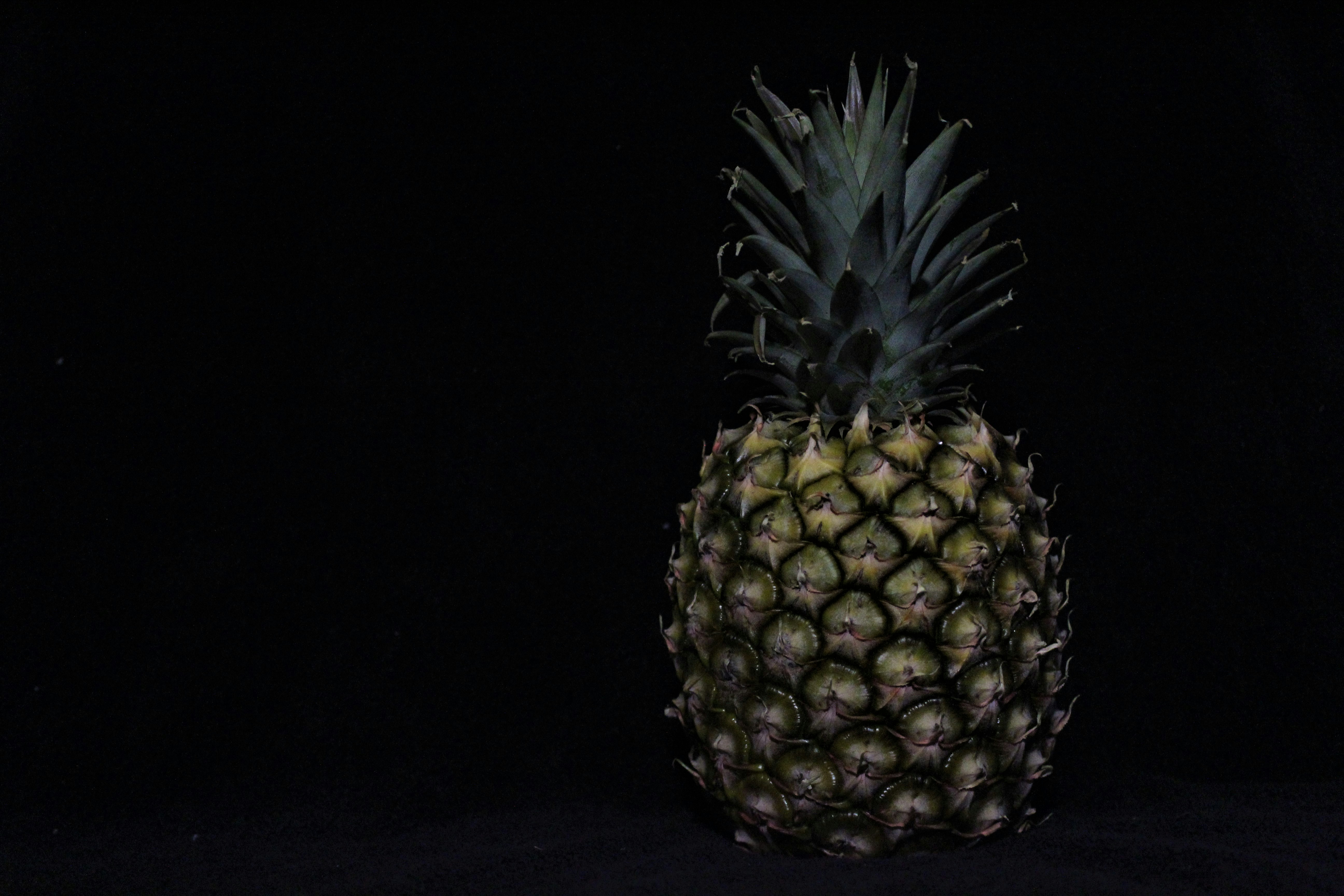 A pineapple stands elegantly against a black backdrop, showcasing its textured skin and vibrant green leaves.