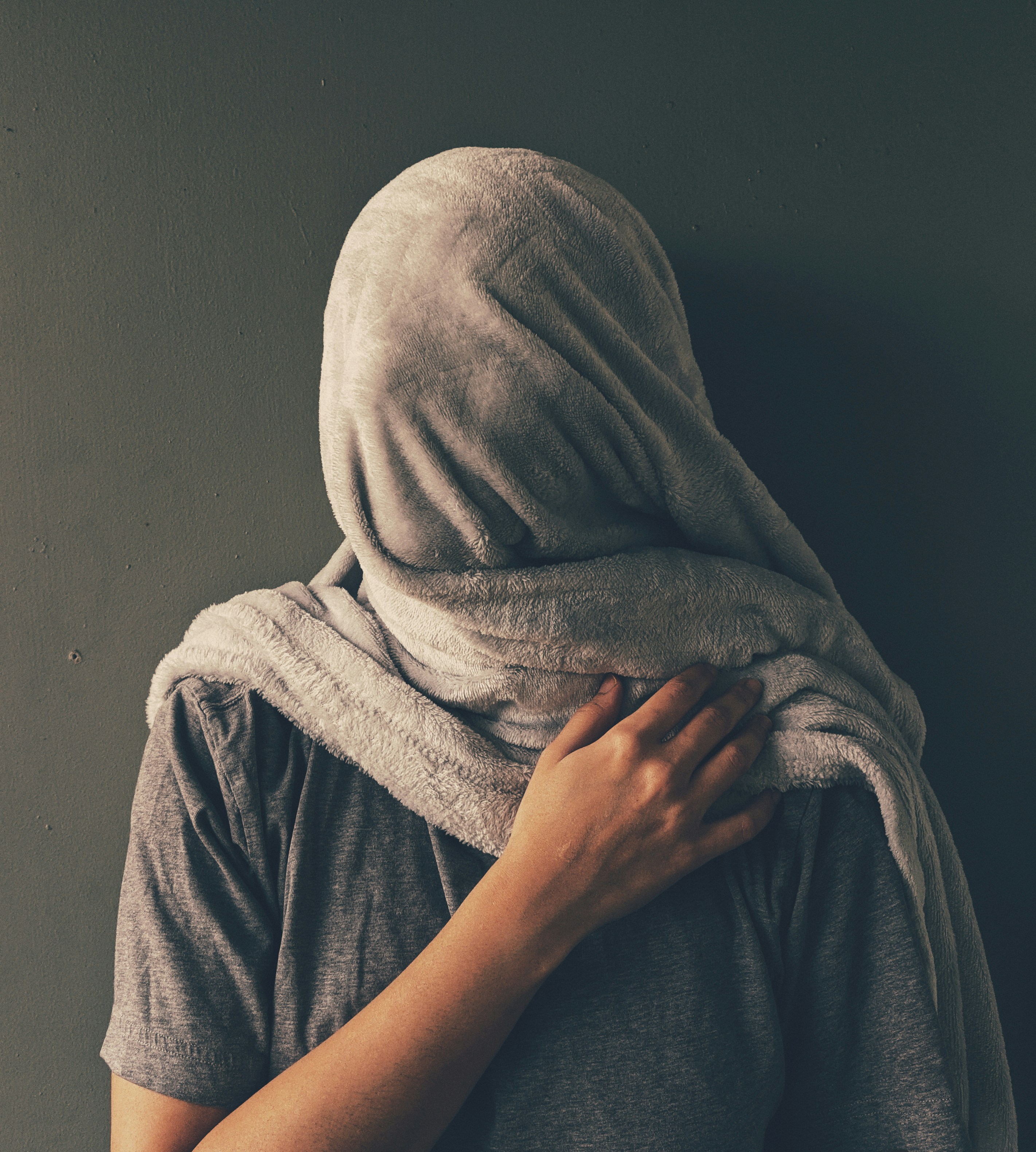 Person draped in a gray fabric obscuring their face, creating a mysterious and contemplative mood.