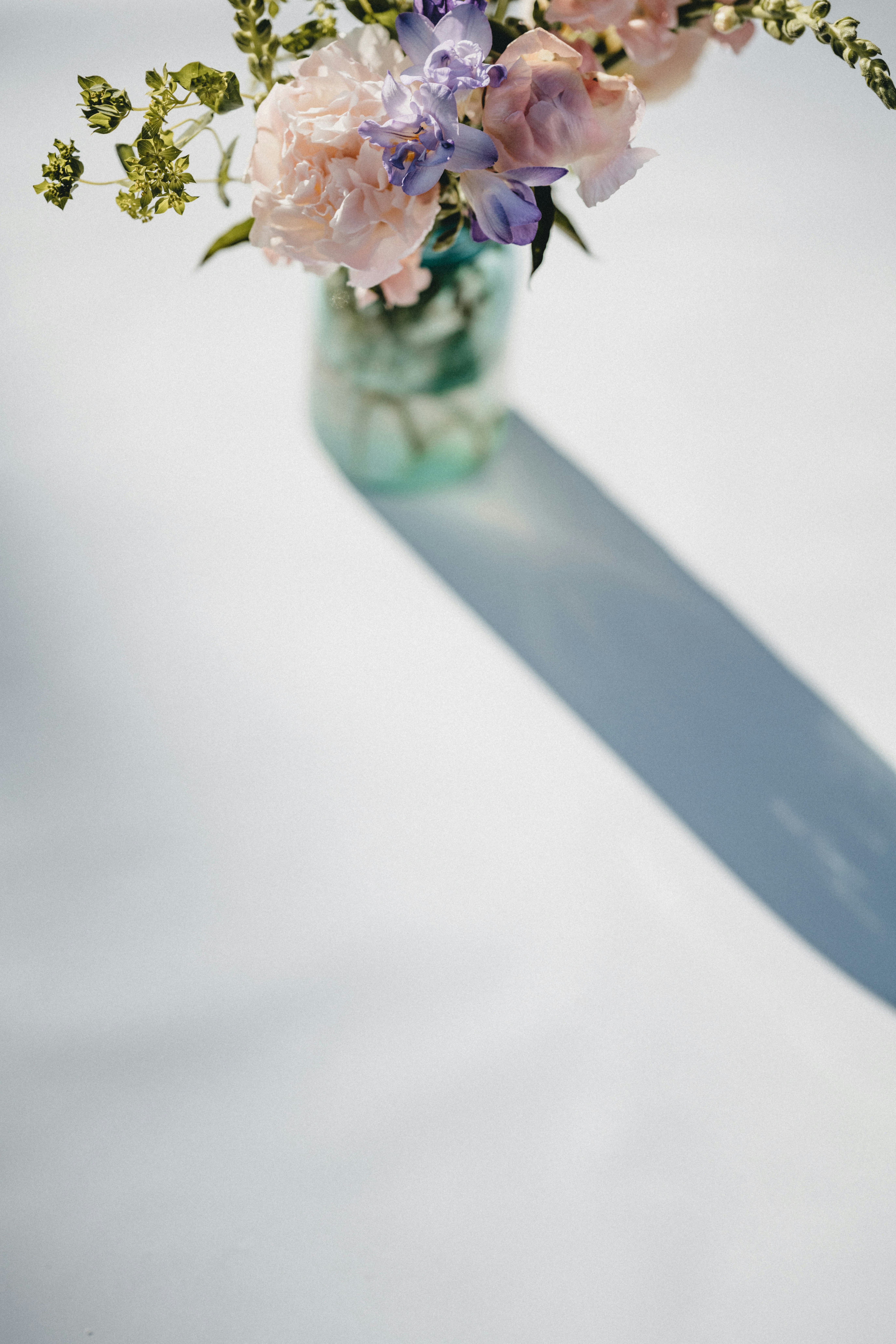 Delicate pastel flowers arranged in a glass vase casting a soft shadow on a white surface.