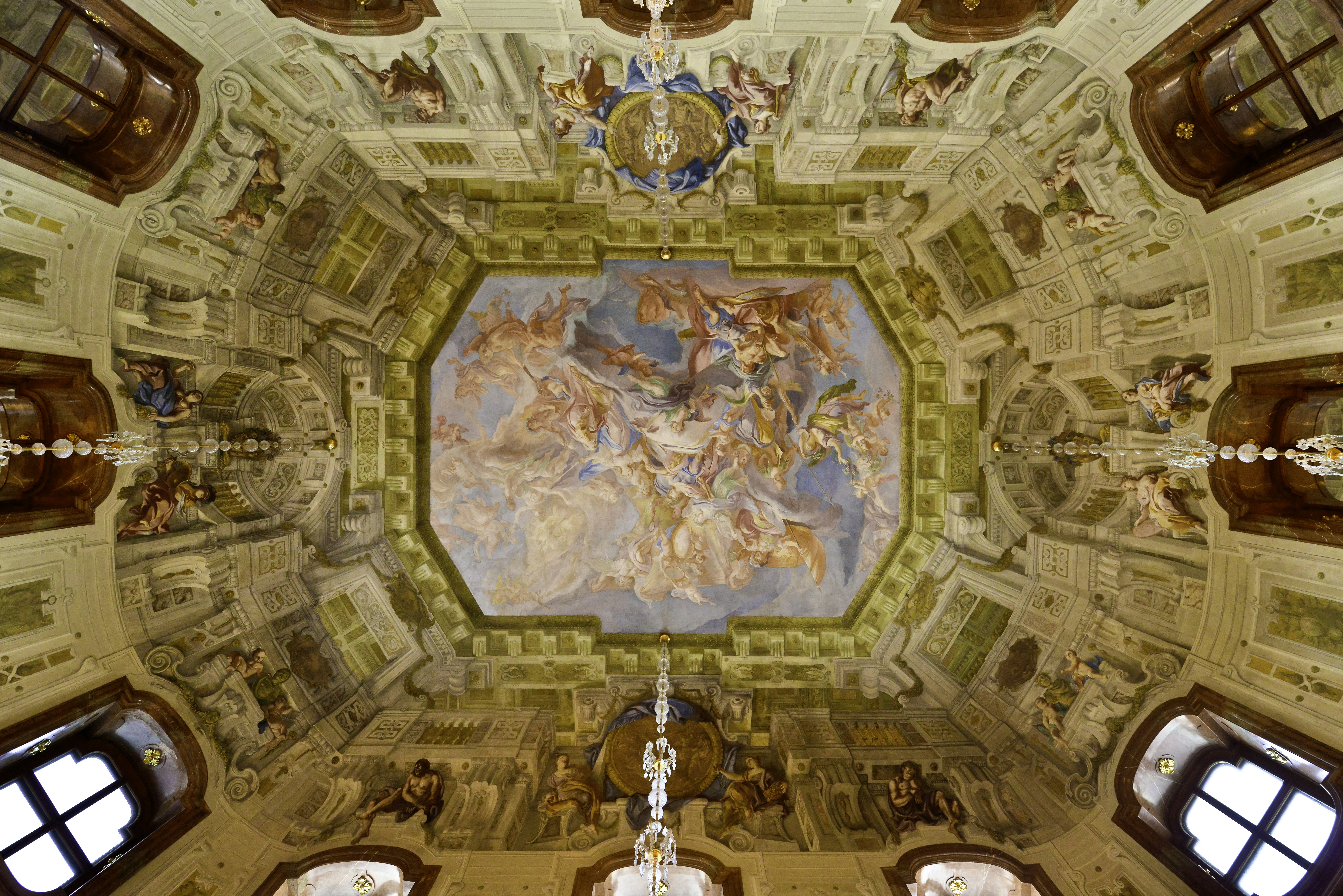 Intricate ceiling fresco depicting mythological figures amidst ornate architectural details. The artwork showcases a blend of colors and forms, drawing the viewer's gaze upward.