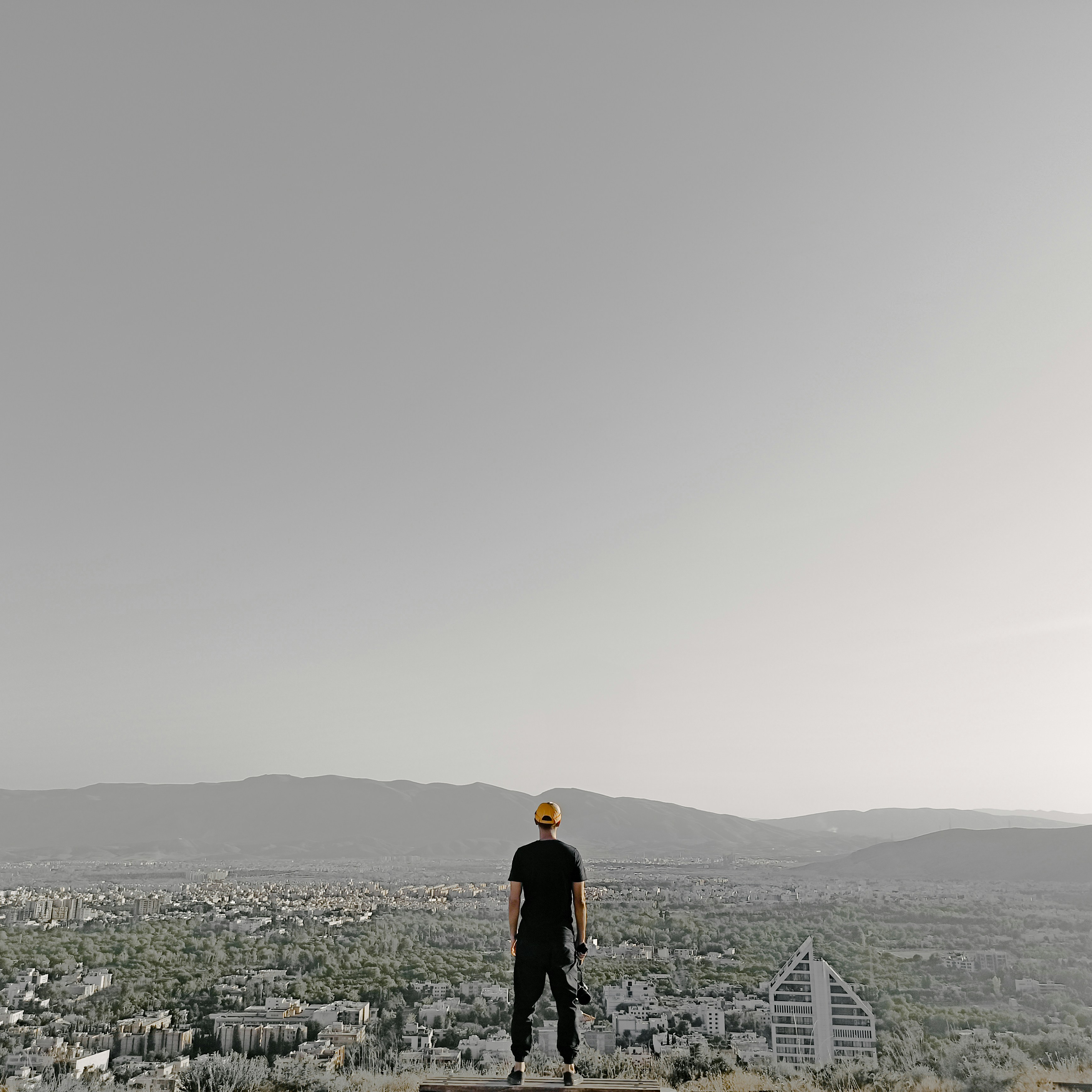 Silhouette of a figure overlooking a sprawling cityscape from a high vantage point, with mountains in the distance. The scene captures a moment of contemplation and exploration.