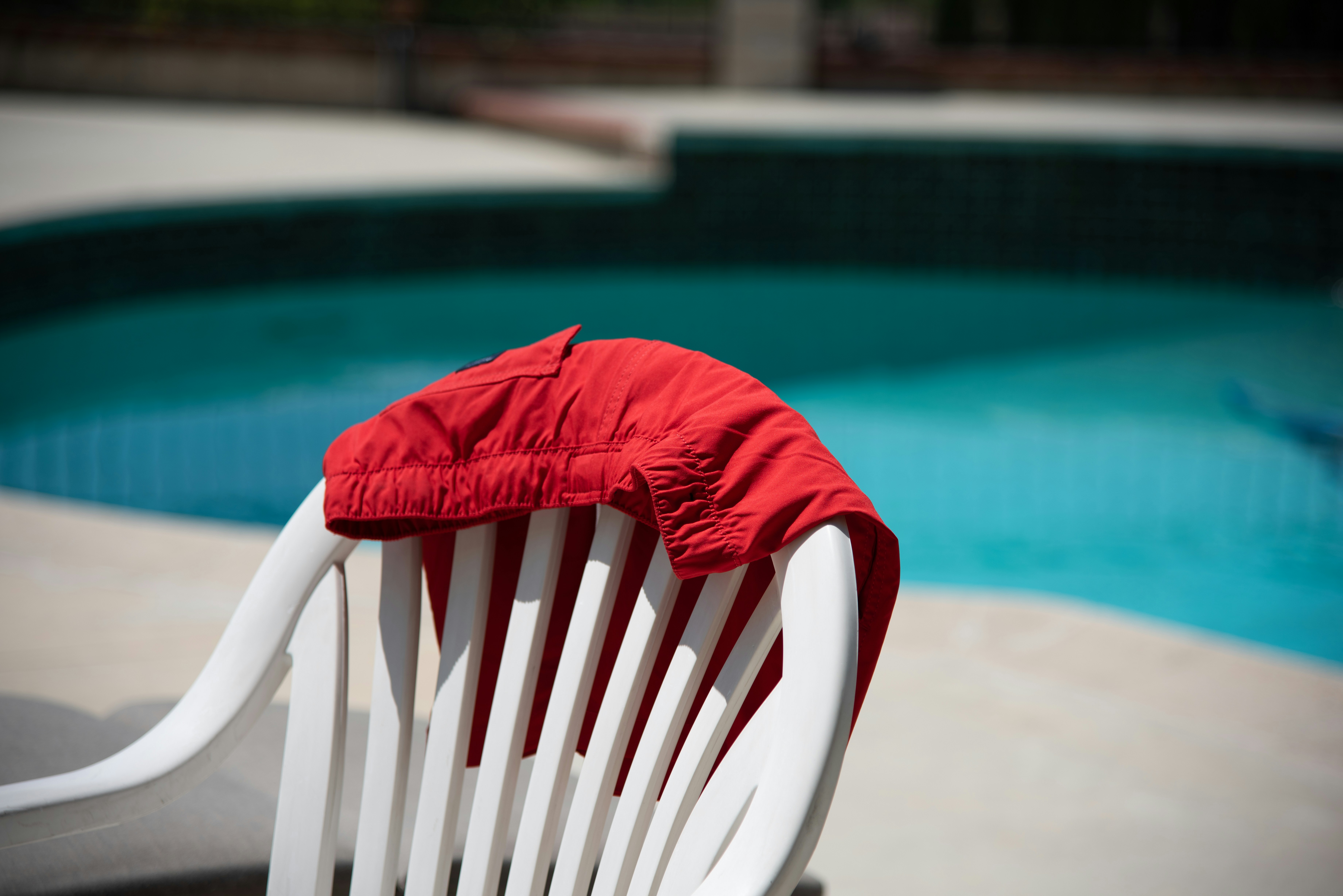 Red swim shorts drying by the pool  | red textile on white plastic chair