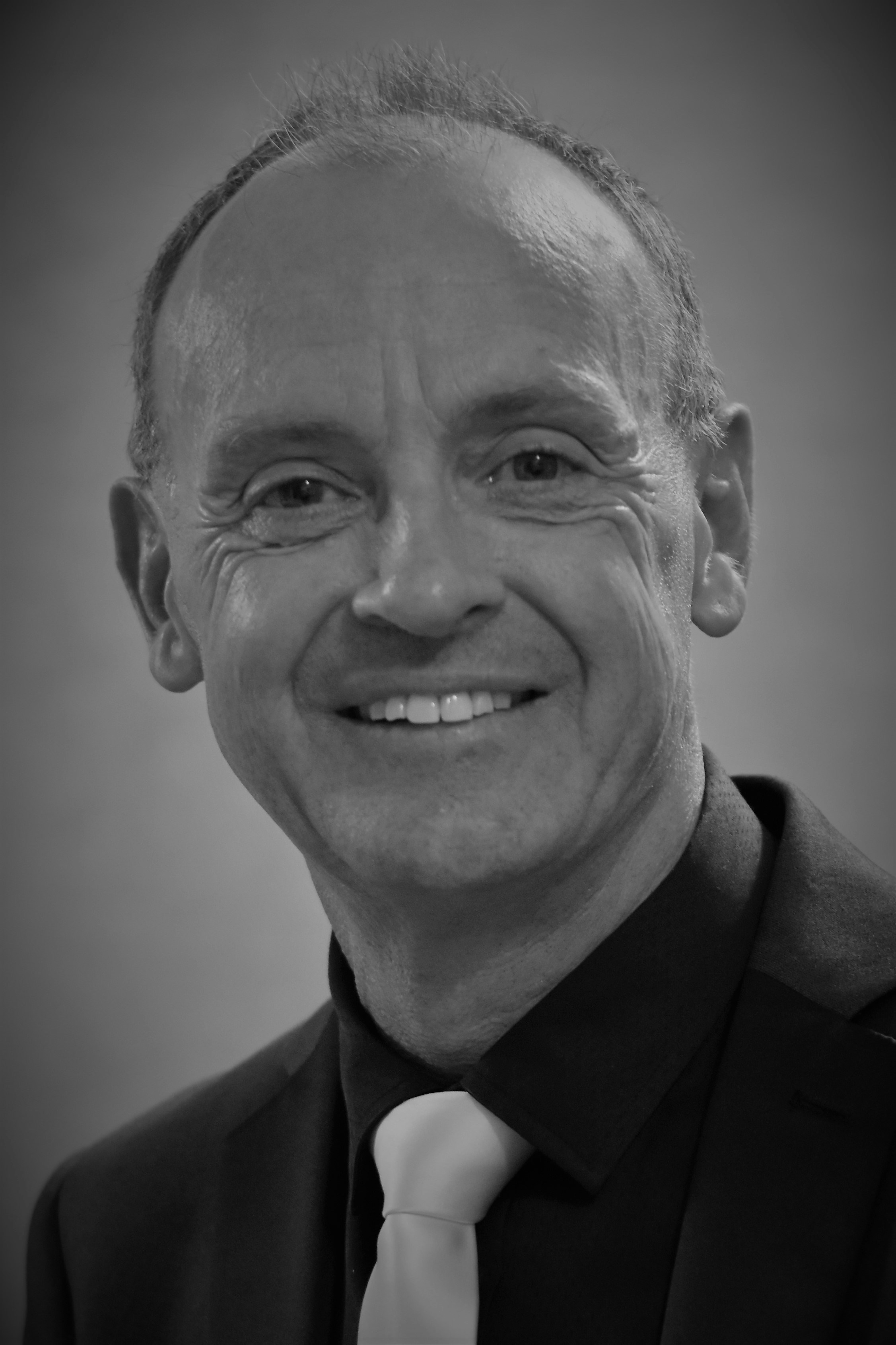 Black and white portrait of a man in a suit with a white tie, smiling warmly.