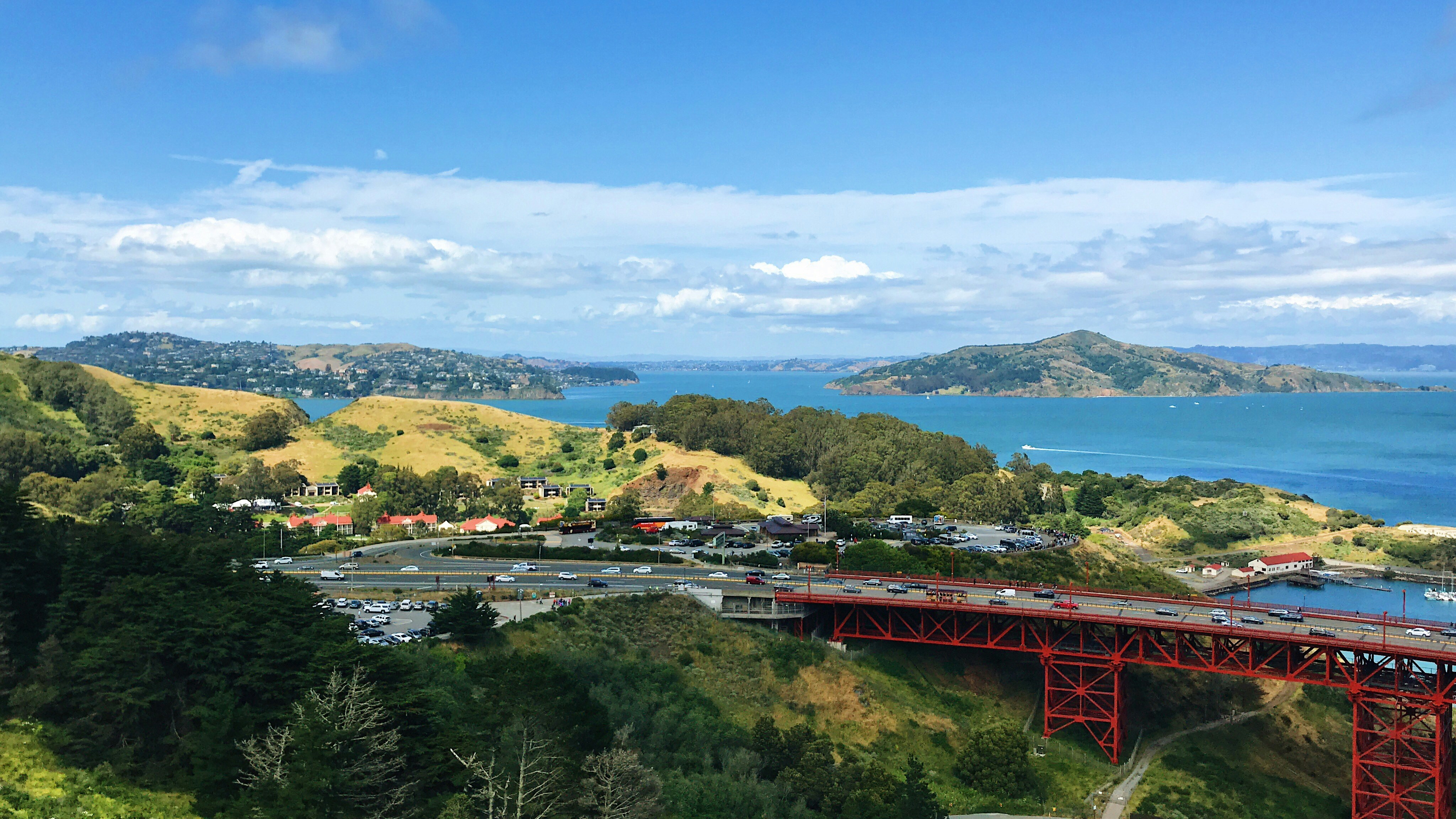 Golden Gate Bridge spanning a lush landscape with rolling hills and blue waters under a bright sky.