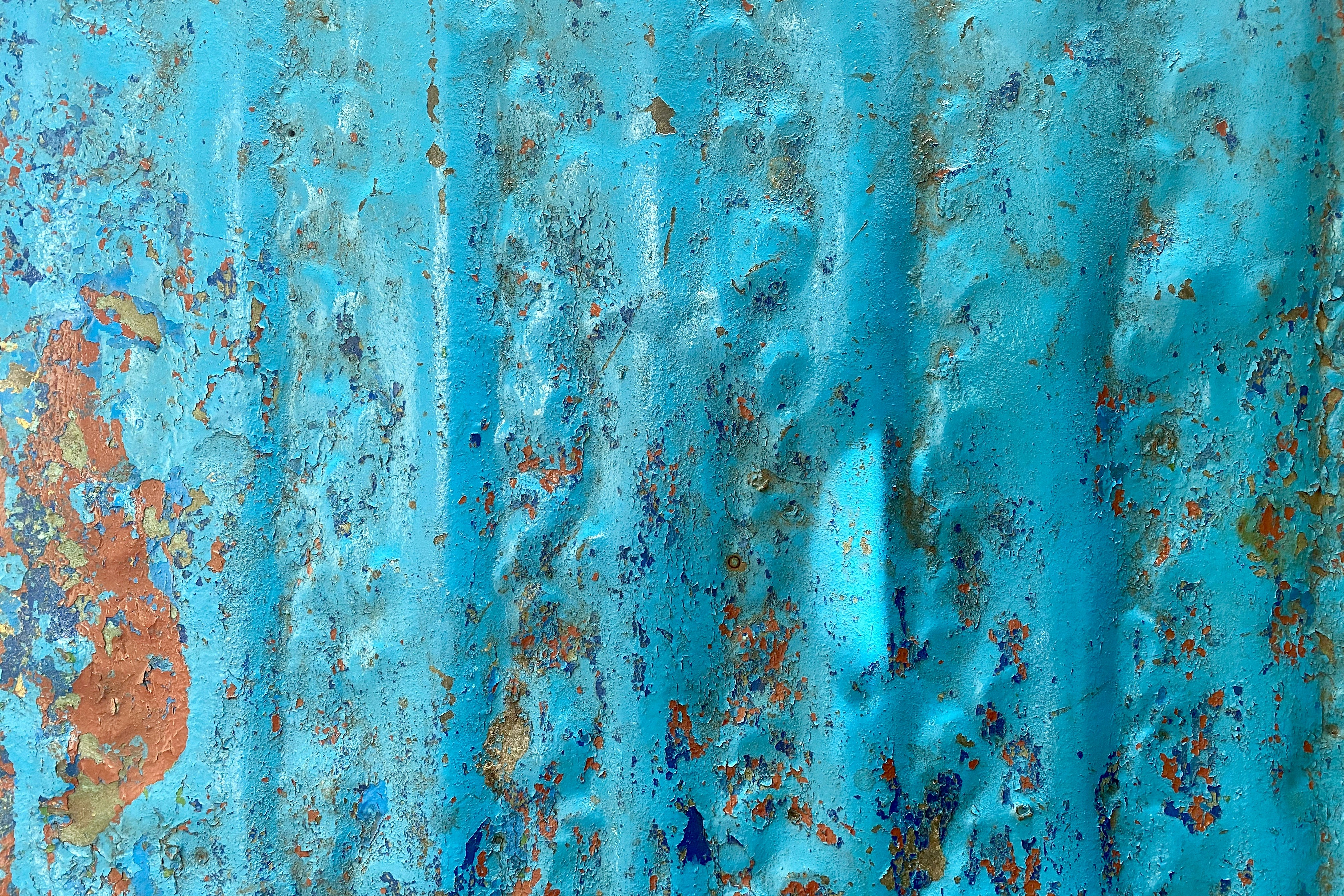 Textured blue surface with rust and peeling paint, showcasing the passage of time and nature's artistry.