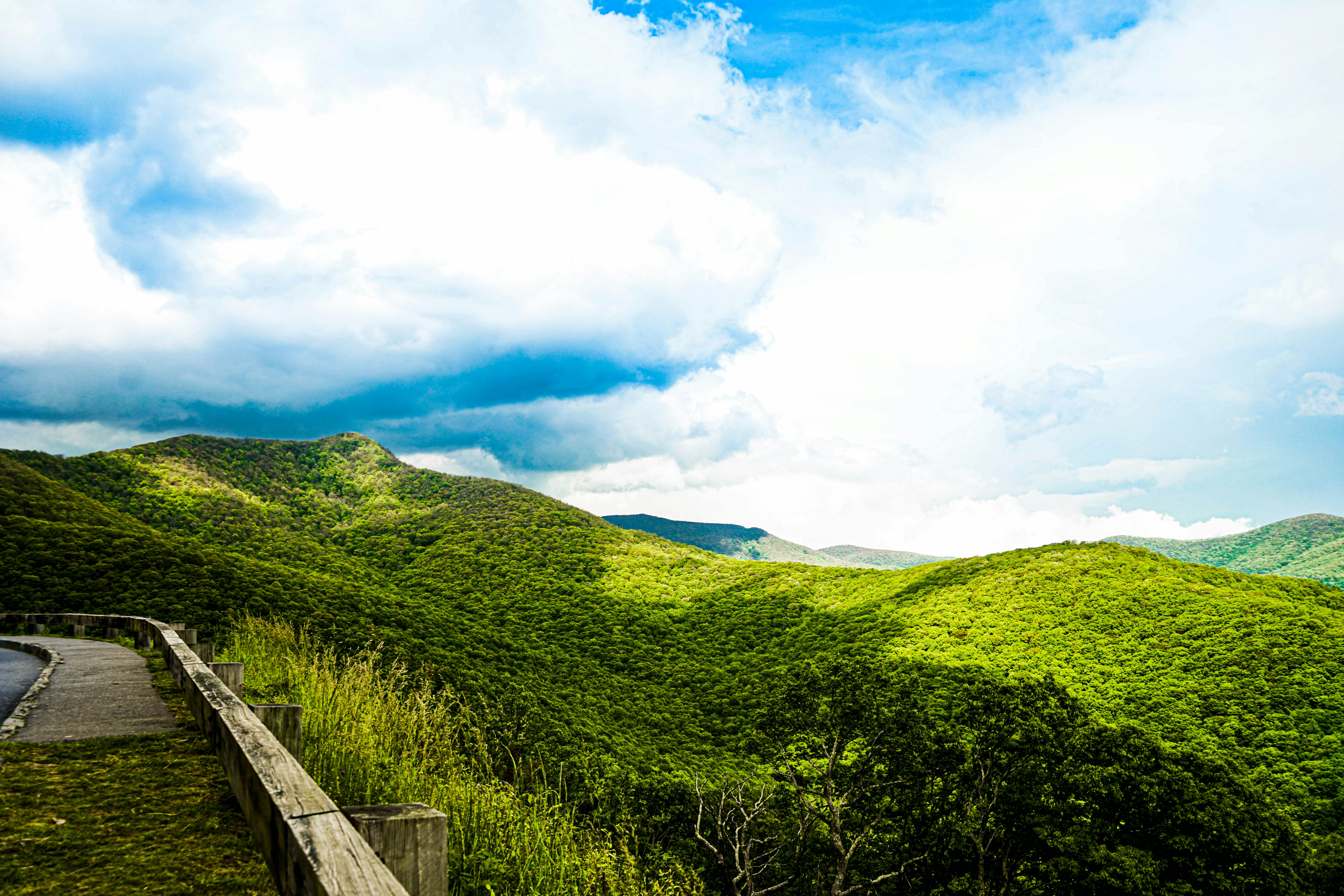Lush green hills with a winding road under a vibrant blue sky and billowing white clouds.
