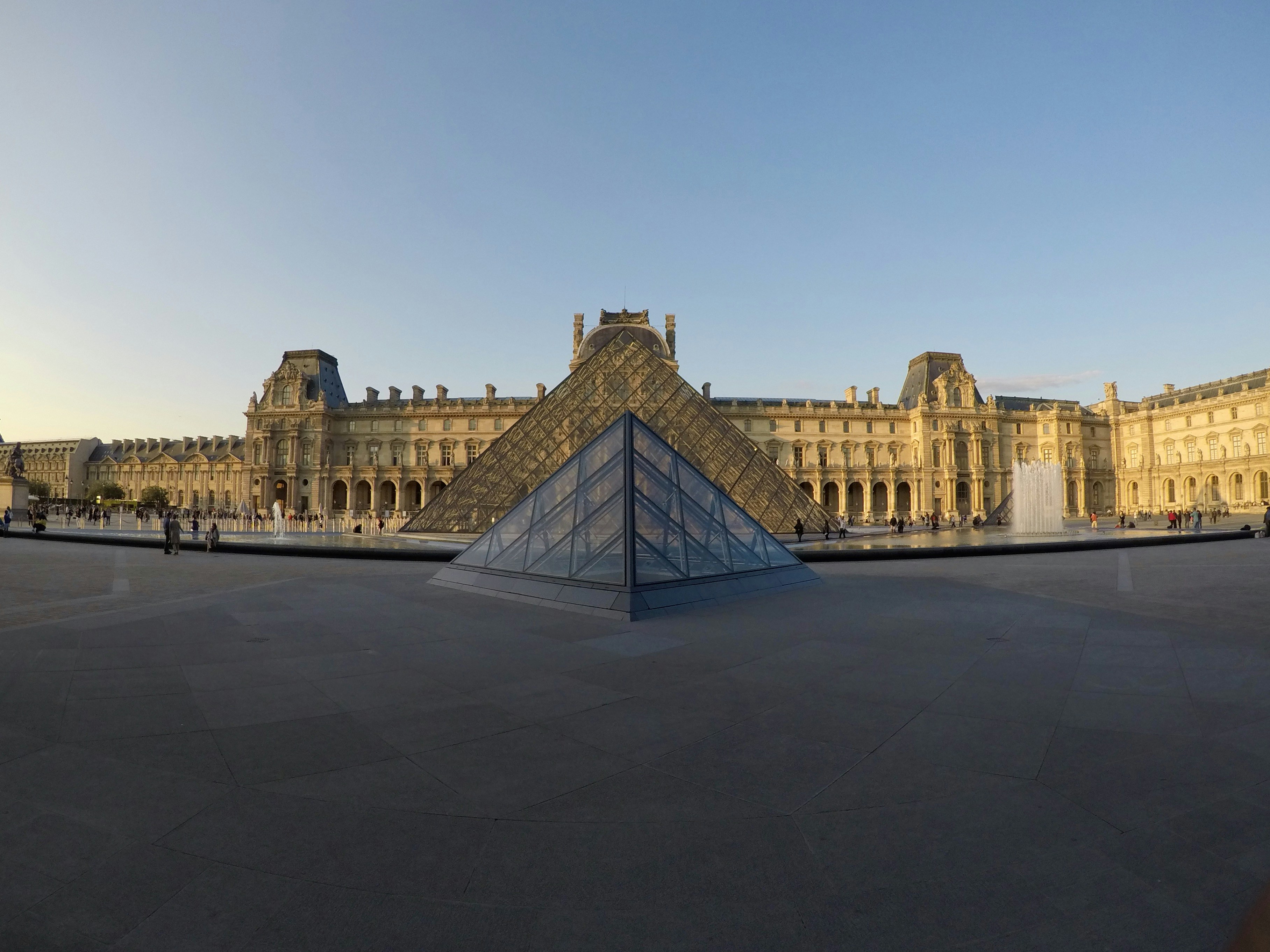 Glass pyramid at the Louvre Museum surrounded by historic architecture under a clear sky.