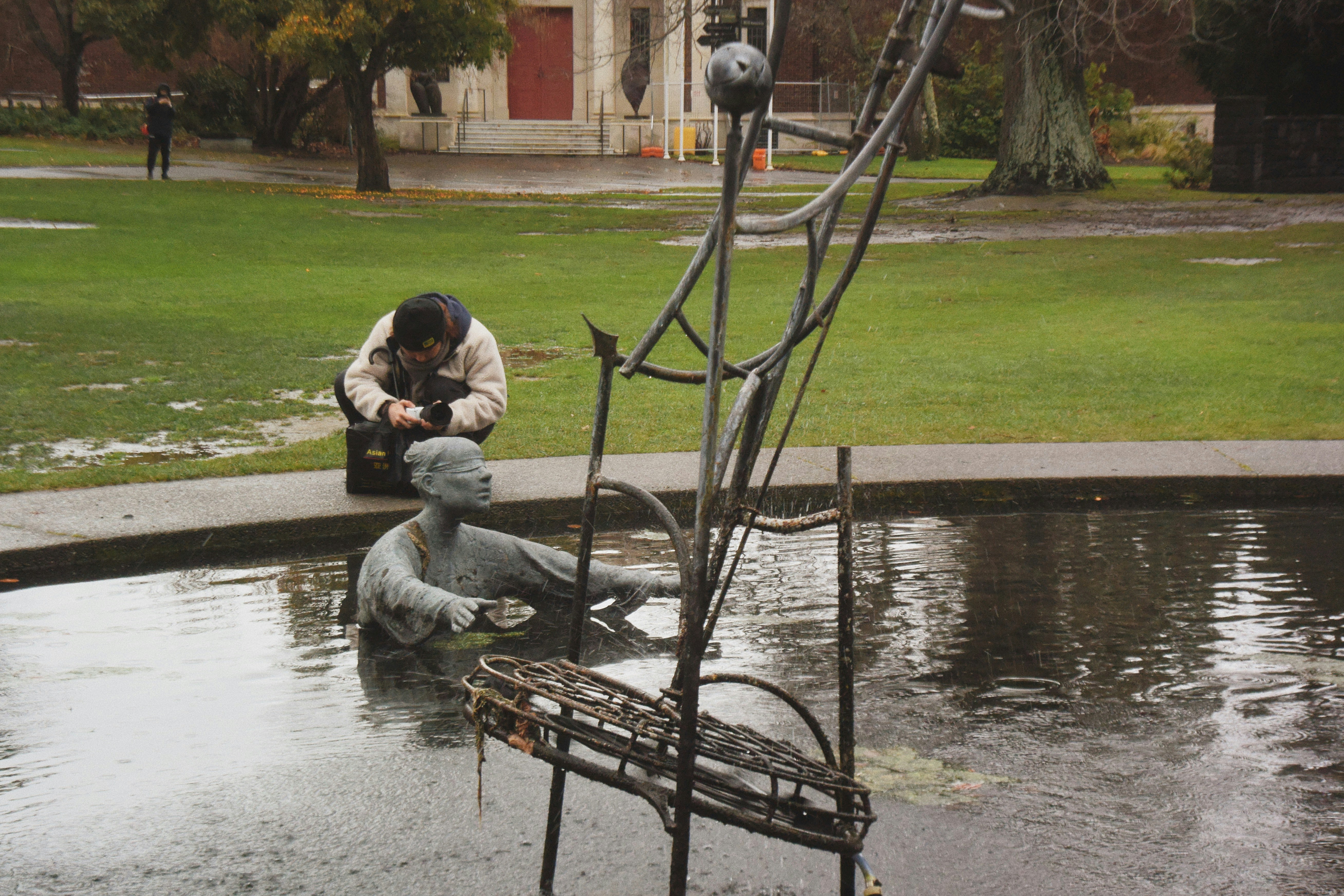 Person photographing a unique water sculpture in a tranquil park setting.