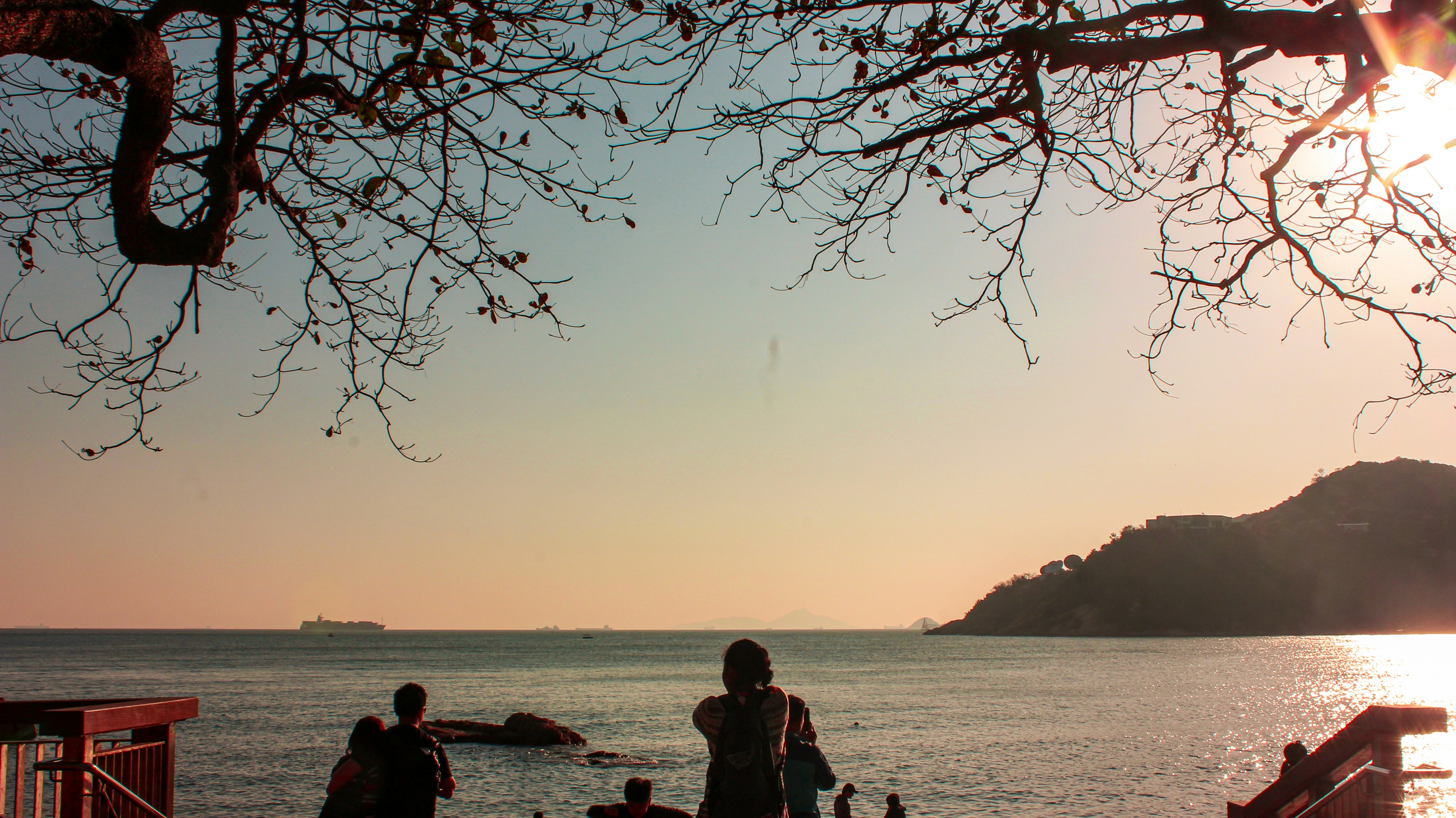 Silhouetted figures enjoy a tranquil evening at the beach as the sun sets over the horizon, casting warm hues across the water.