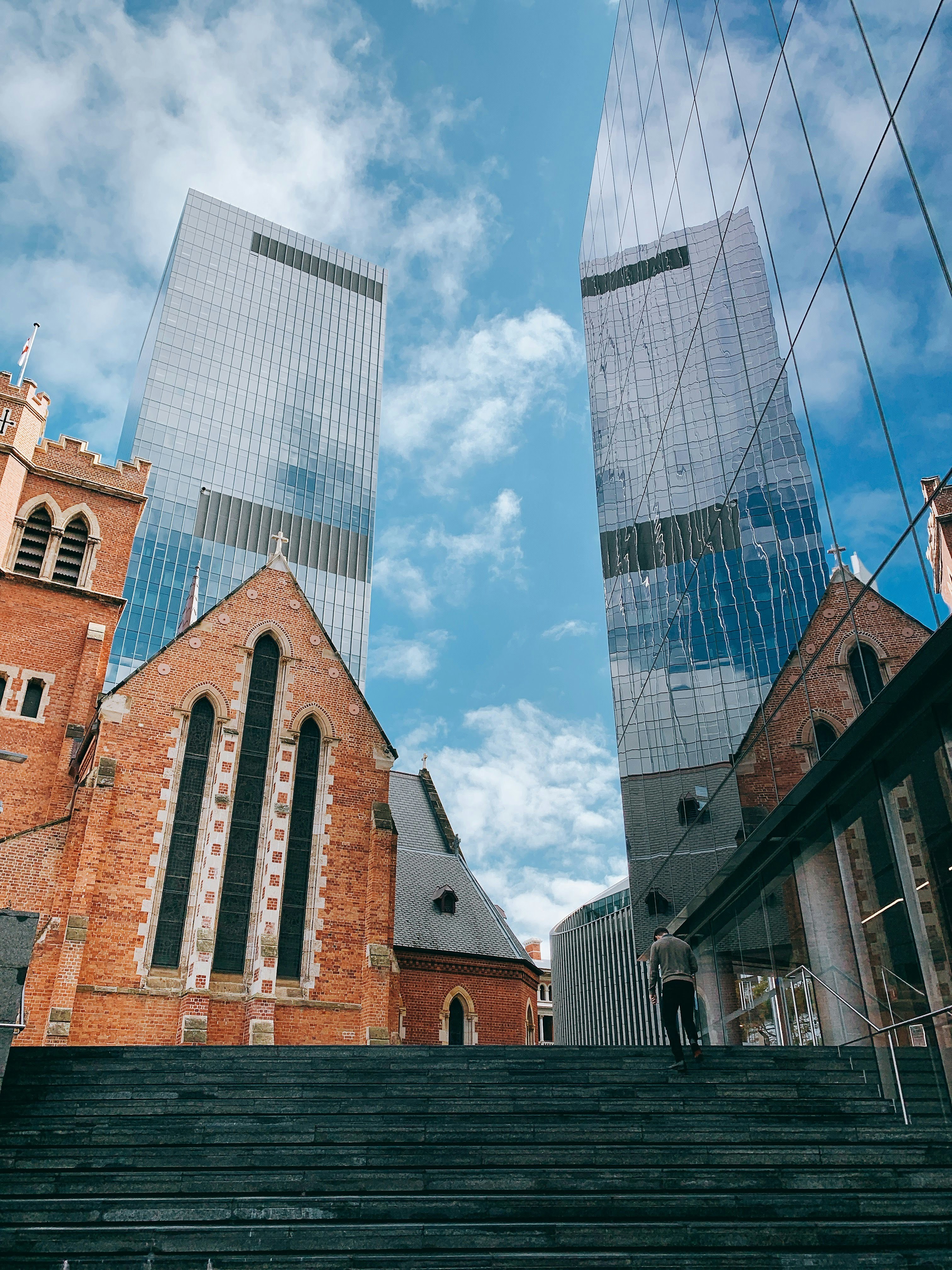 Historic brown brick church juxtaposed against towering glass skyscrapers under a bright blue sky.