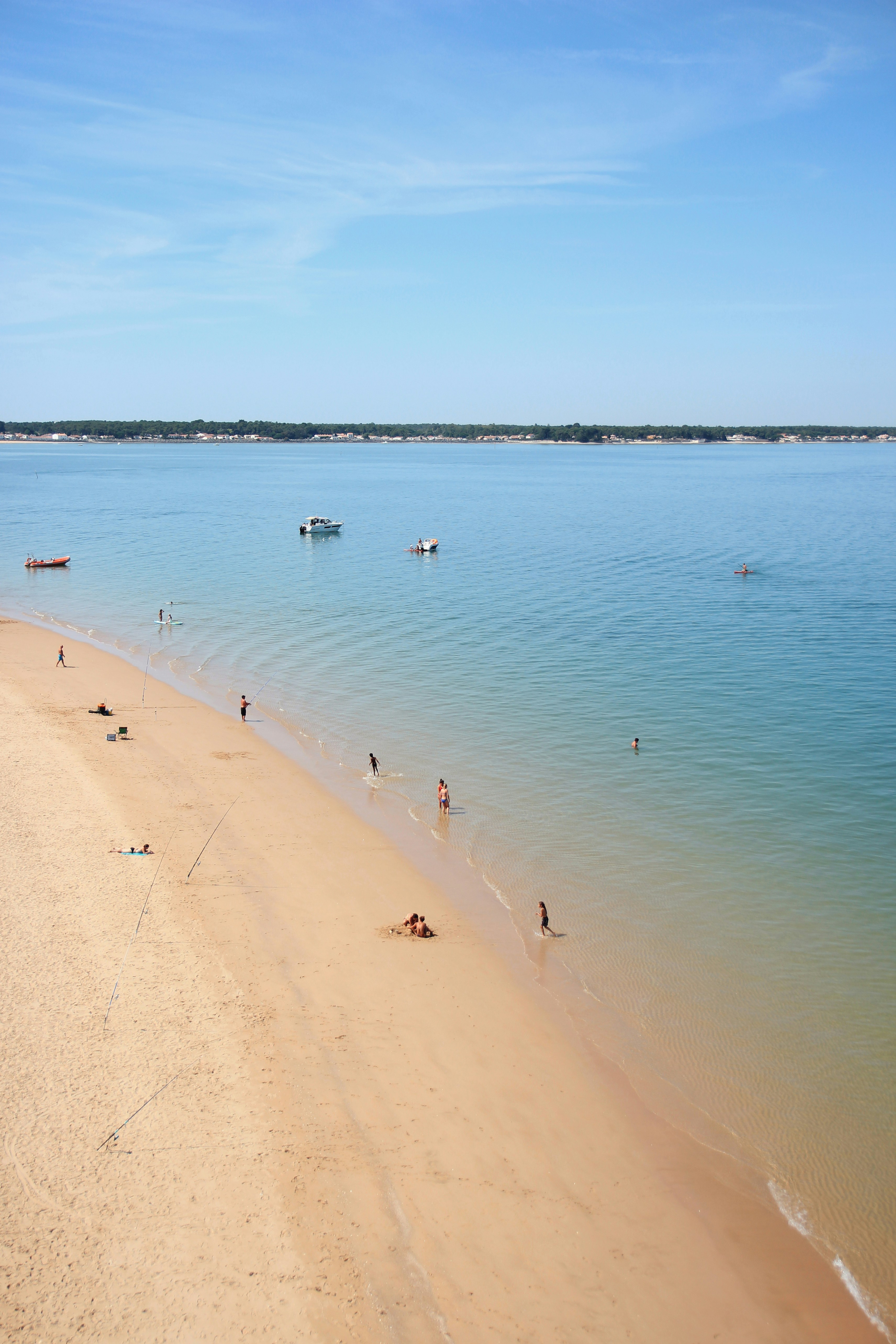 Azure Shoreline: Sunlit Beach, Swimmers, and Distant Boats on Calm Waters