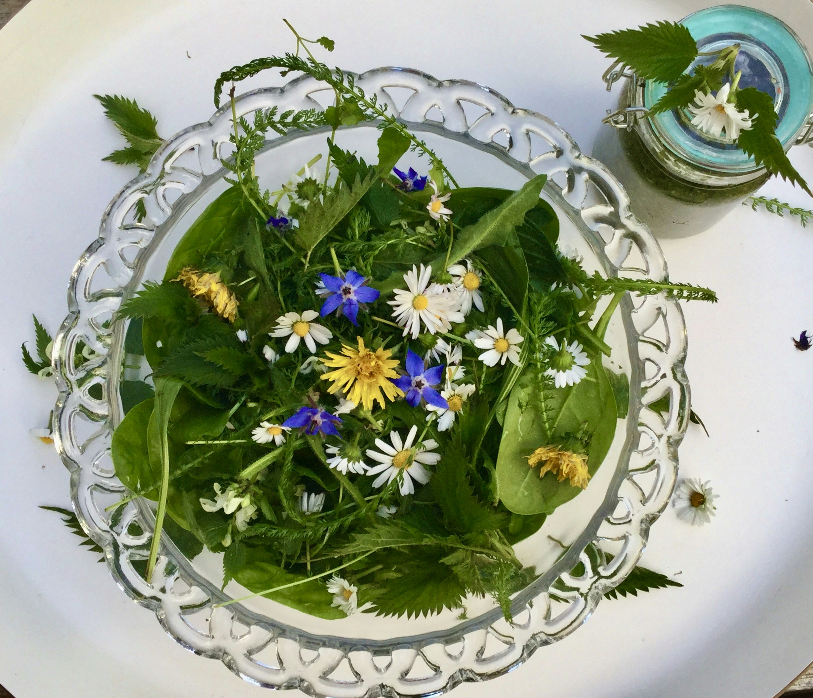 Vibrant salad featuring a mix of fresh greens and wildflowers, arranged elegantly in a decorative bowl, accompanied by a small jar of dressing.