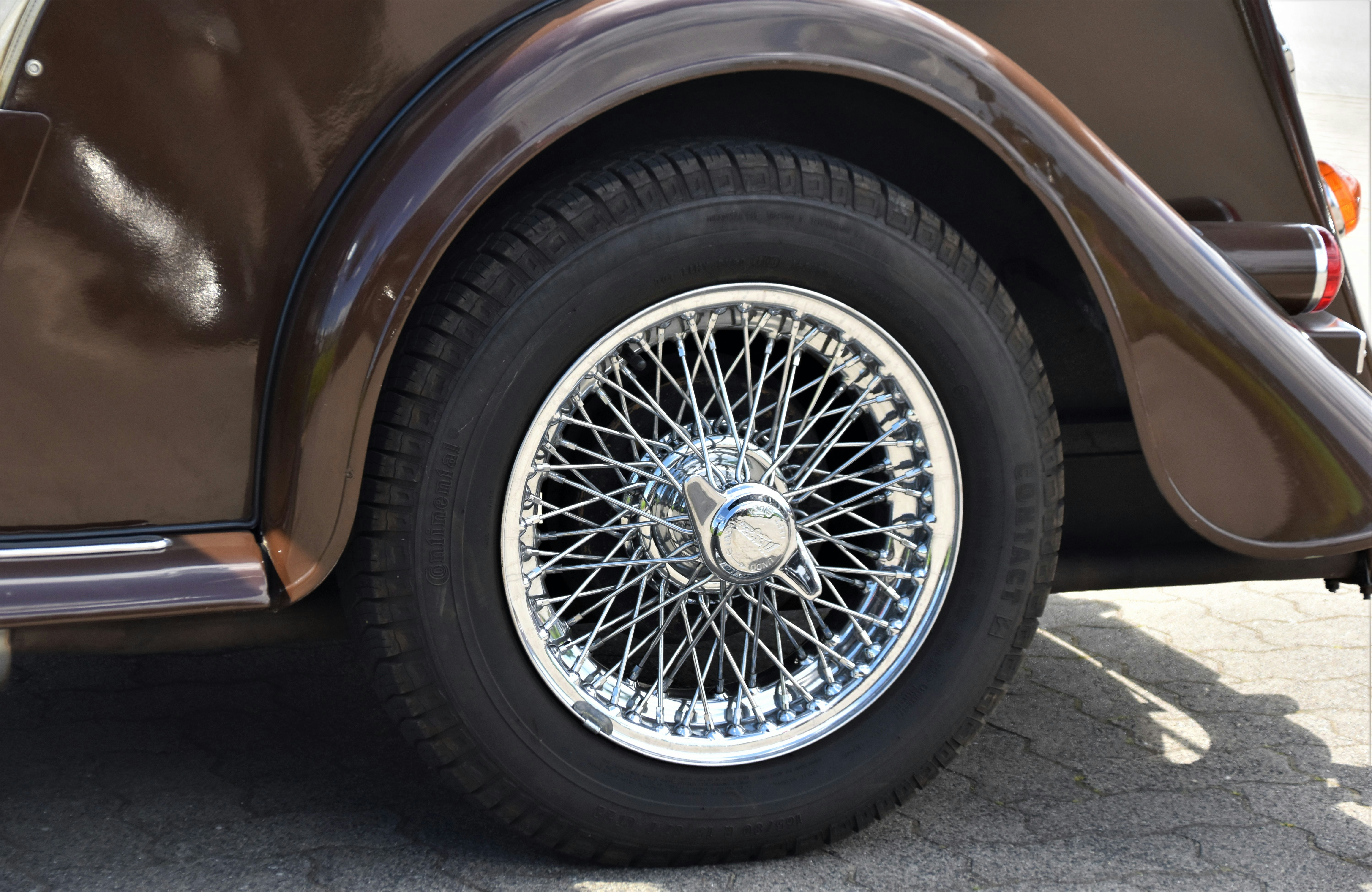 Close-up of a vintage car's wire-spoke wheel, showcasing intricate design and polished chrome accents.