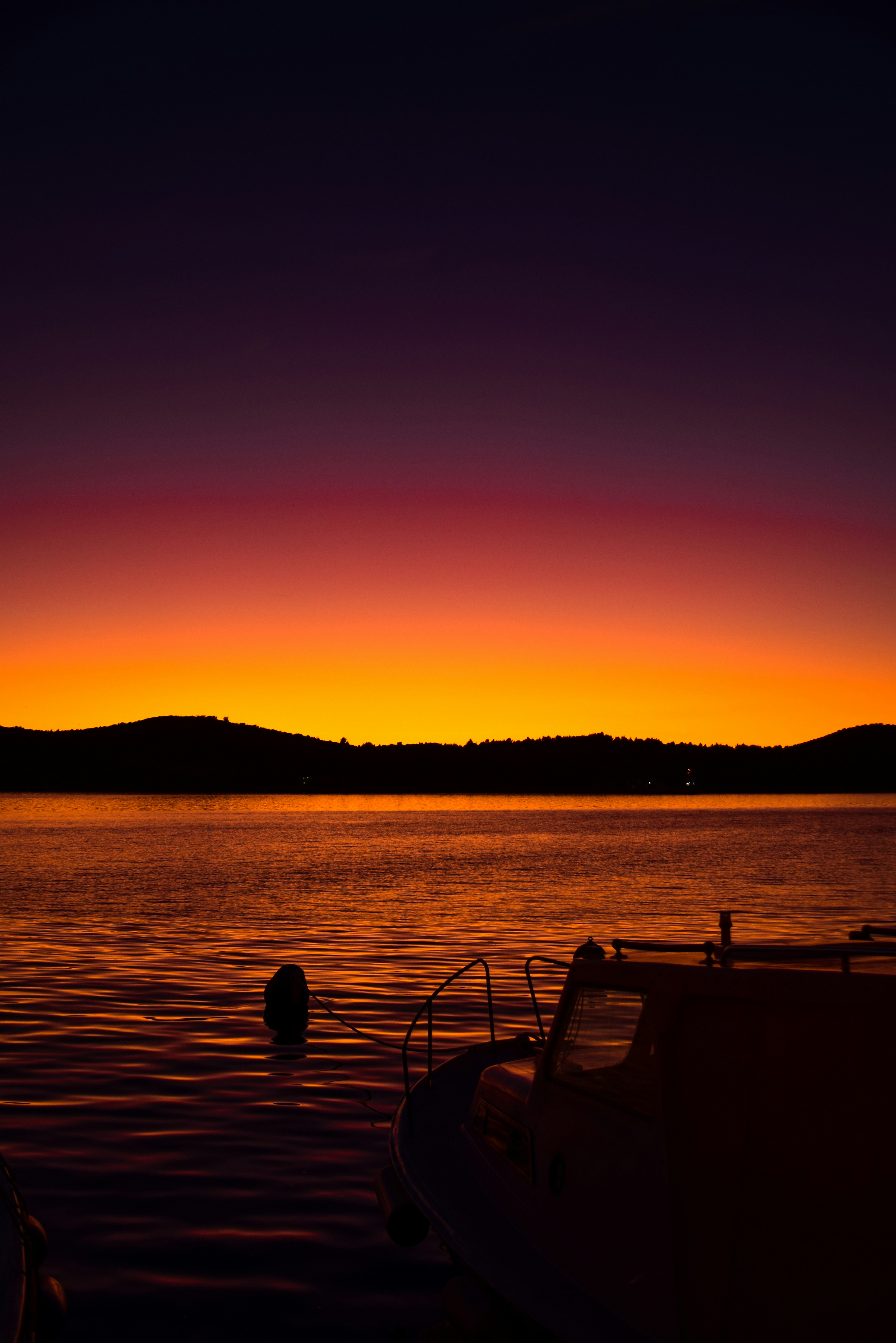 Silhouette of a boat against a vibrant sunset over a calm lake.