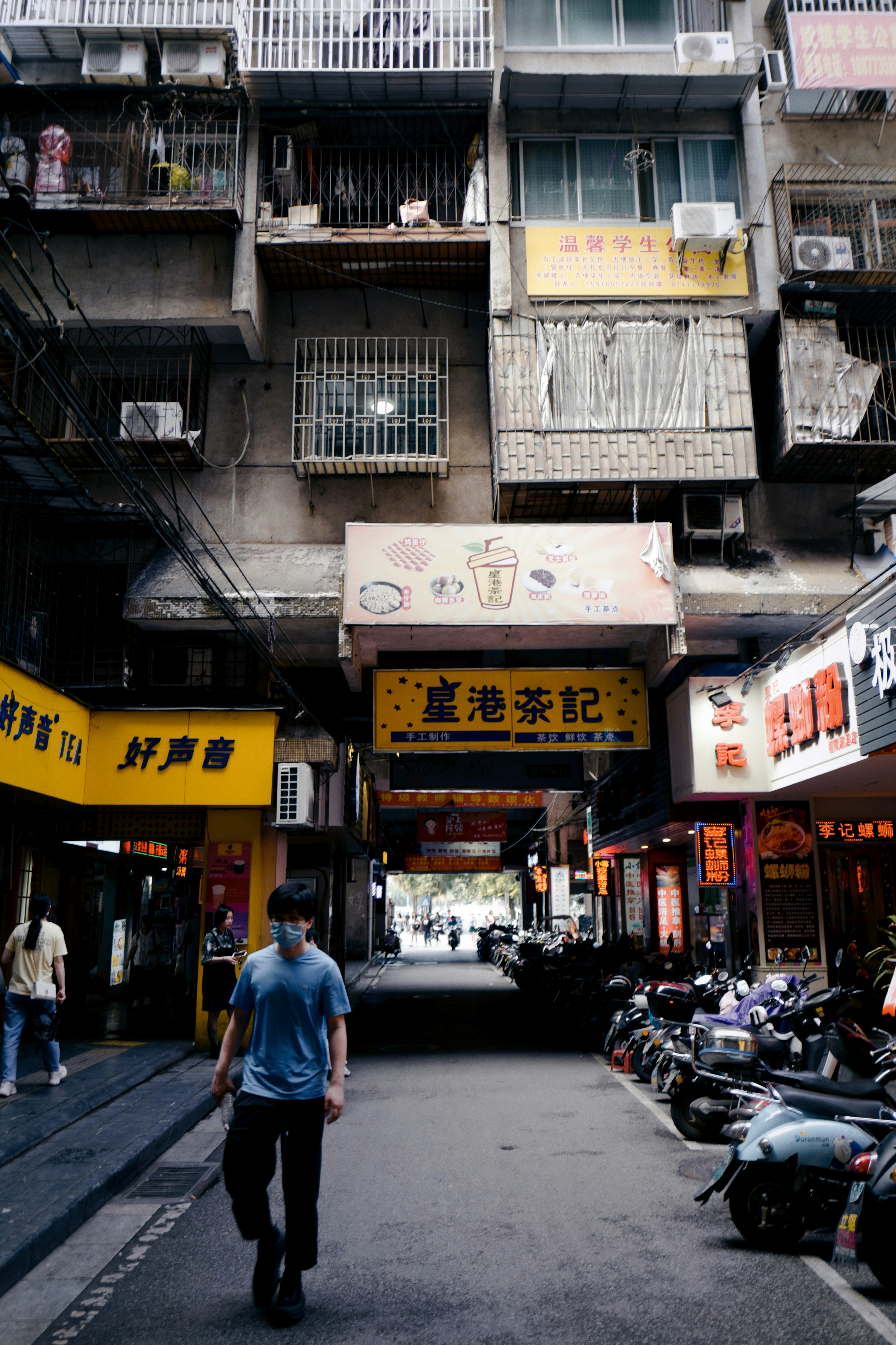 An urban alleyway bustling with activity, featuring vibrant storefronts and a lone pedestrian walking by. The scene captures the essence of everyday city life.
