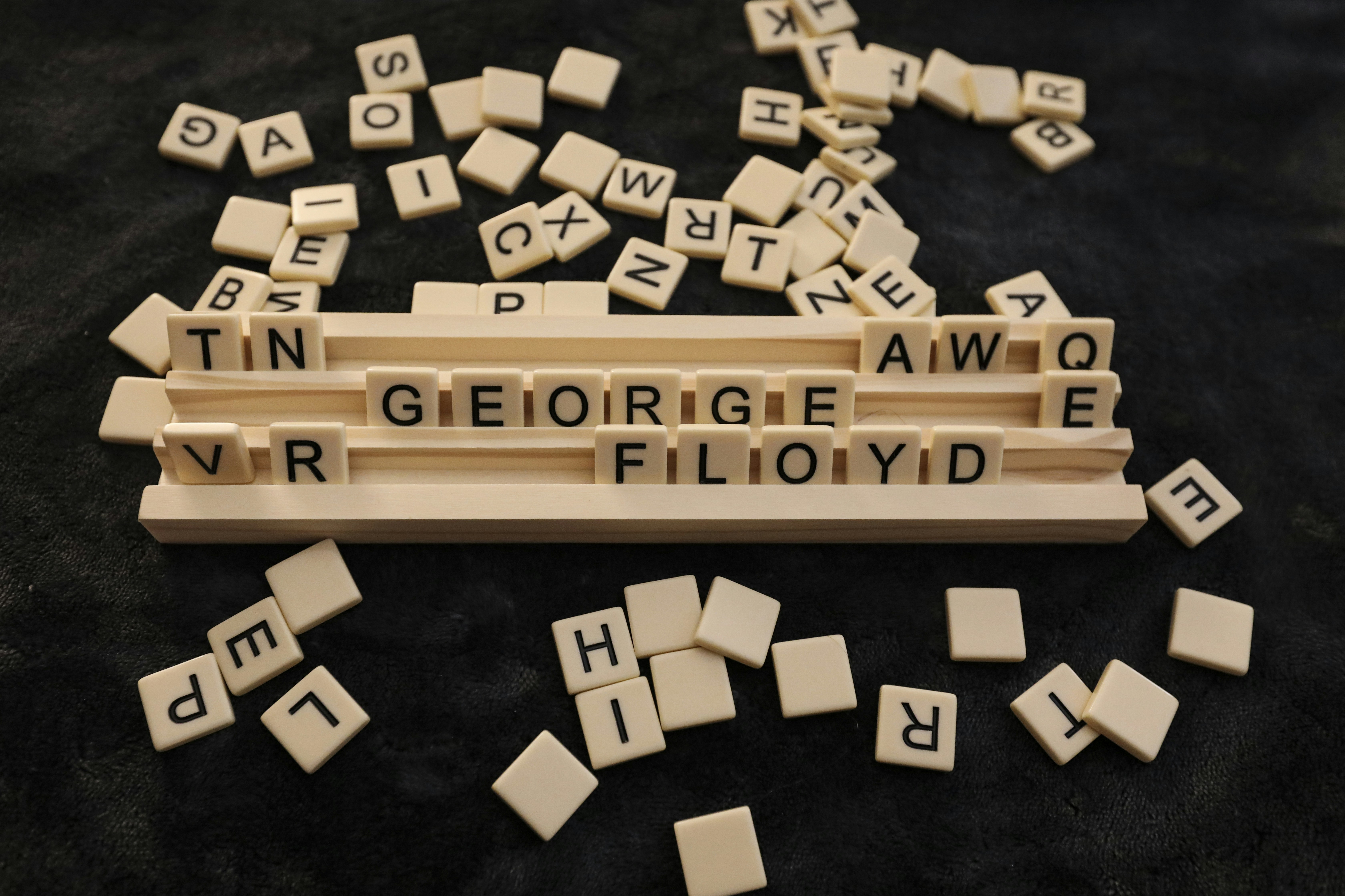 Scrabble tiles arranged to spell 'GEORGE FLOYD' on a dark surface, symbolizing remembrance and reflection.
