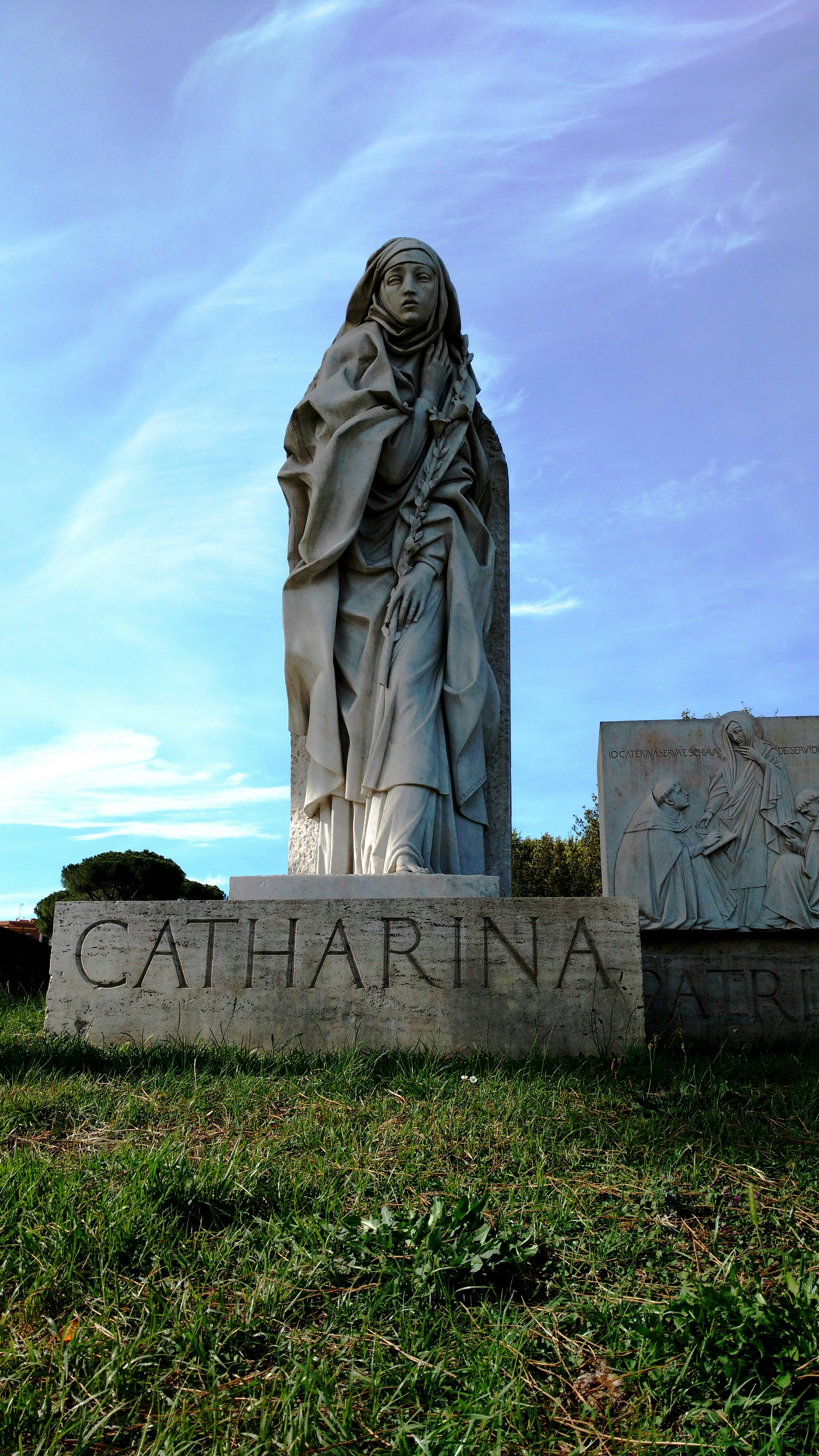 A marble statue named Catharina stands on a stone pedestal with the inscription 'CATHARINA,' set against a bright blue sky.