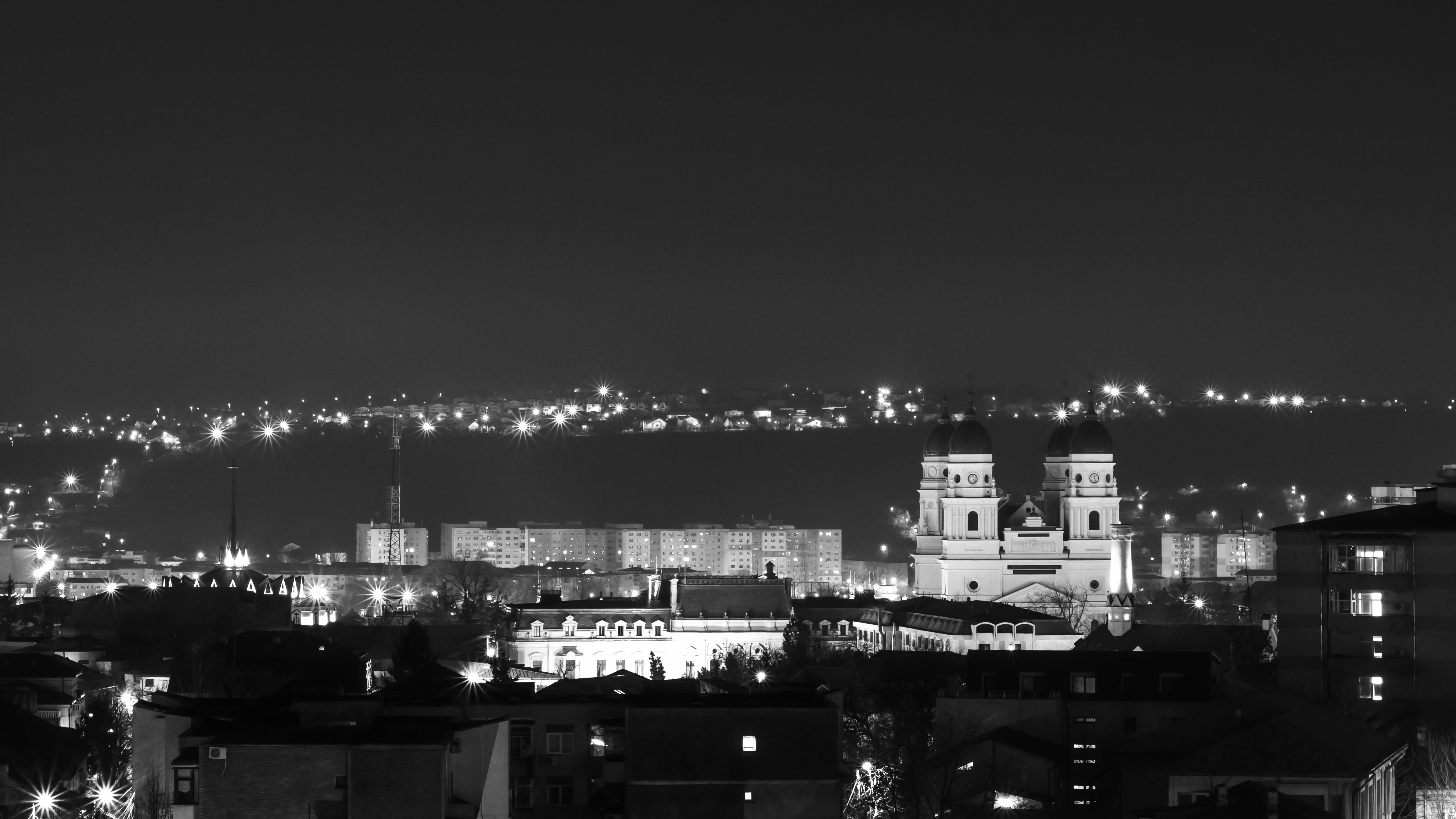 Black and white cityscape with illuminated cathedral and distant city lights at night.