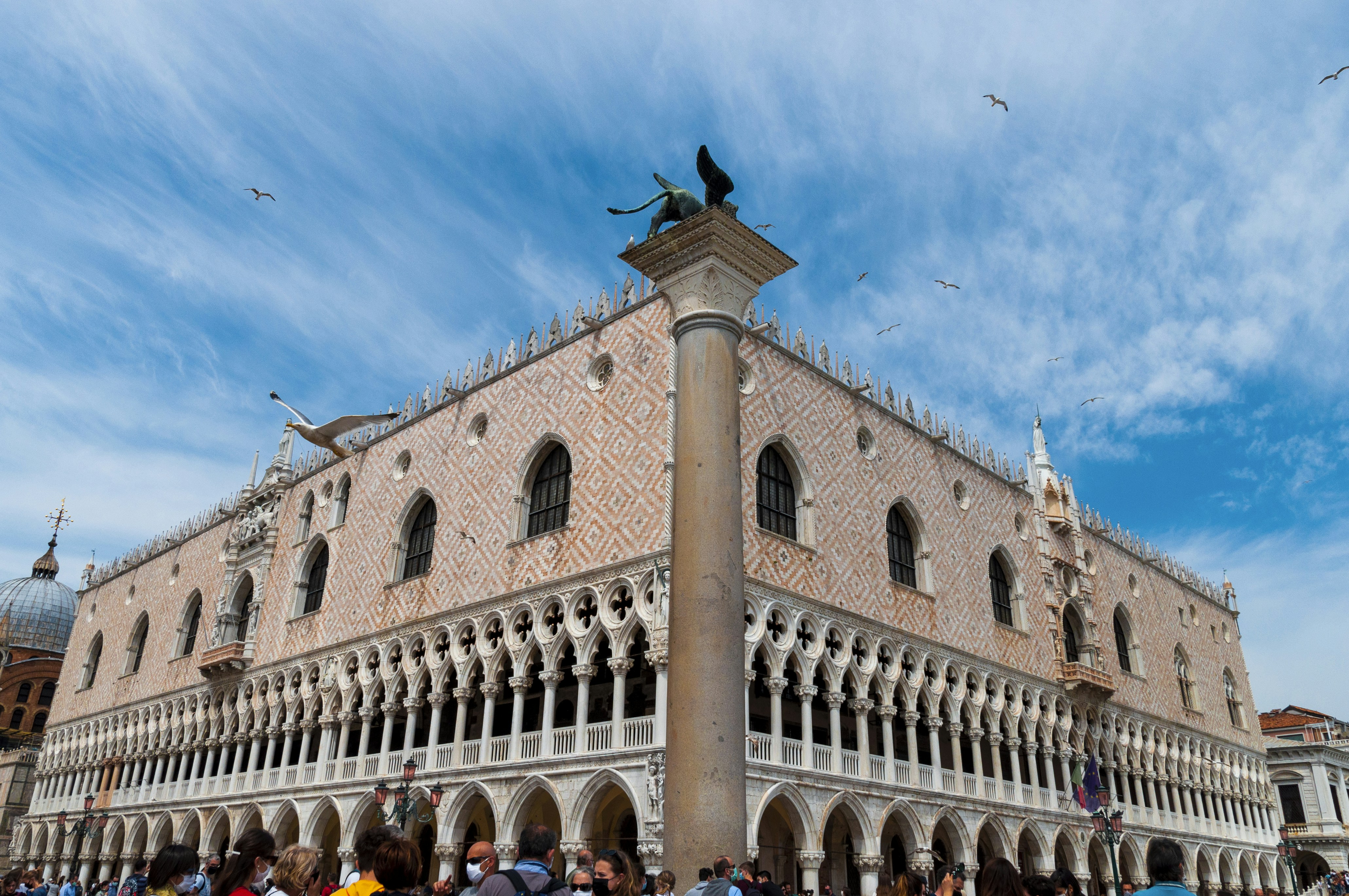 Crowd walking near the historic Doge's Palace in Venice under a vibrant blue sky.
