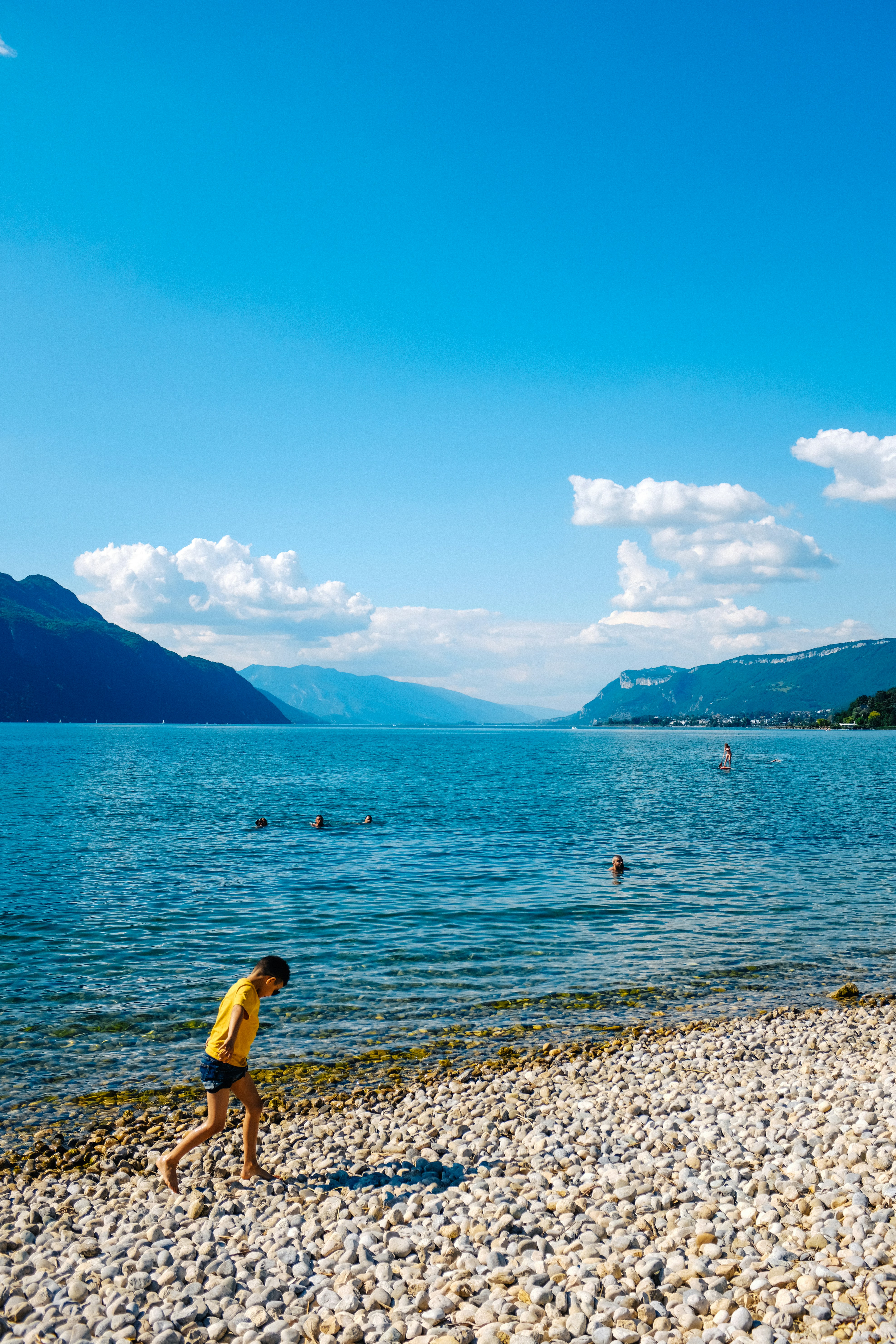 Yellow-Shirt Wanderer on a Pebble Beach Beneath an Alpine Blue Sky